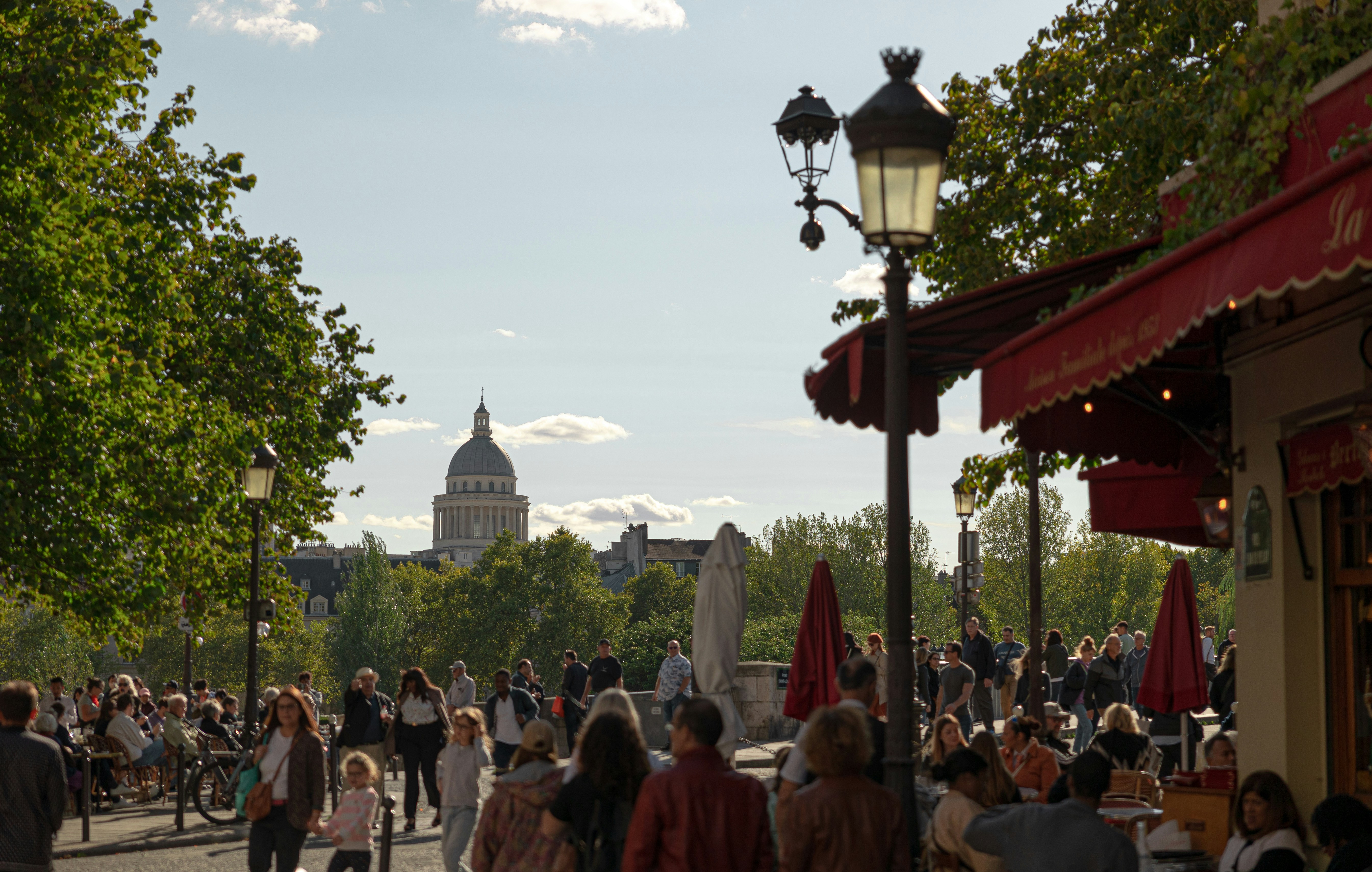 City Square Pulse: Sunlit Crowd, Café Edges, and a Distant Dome