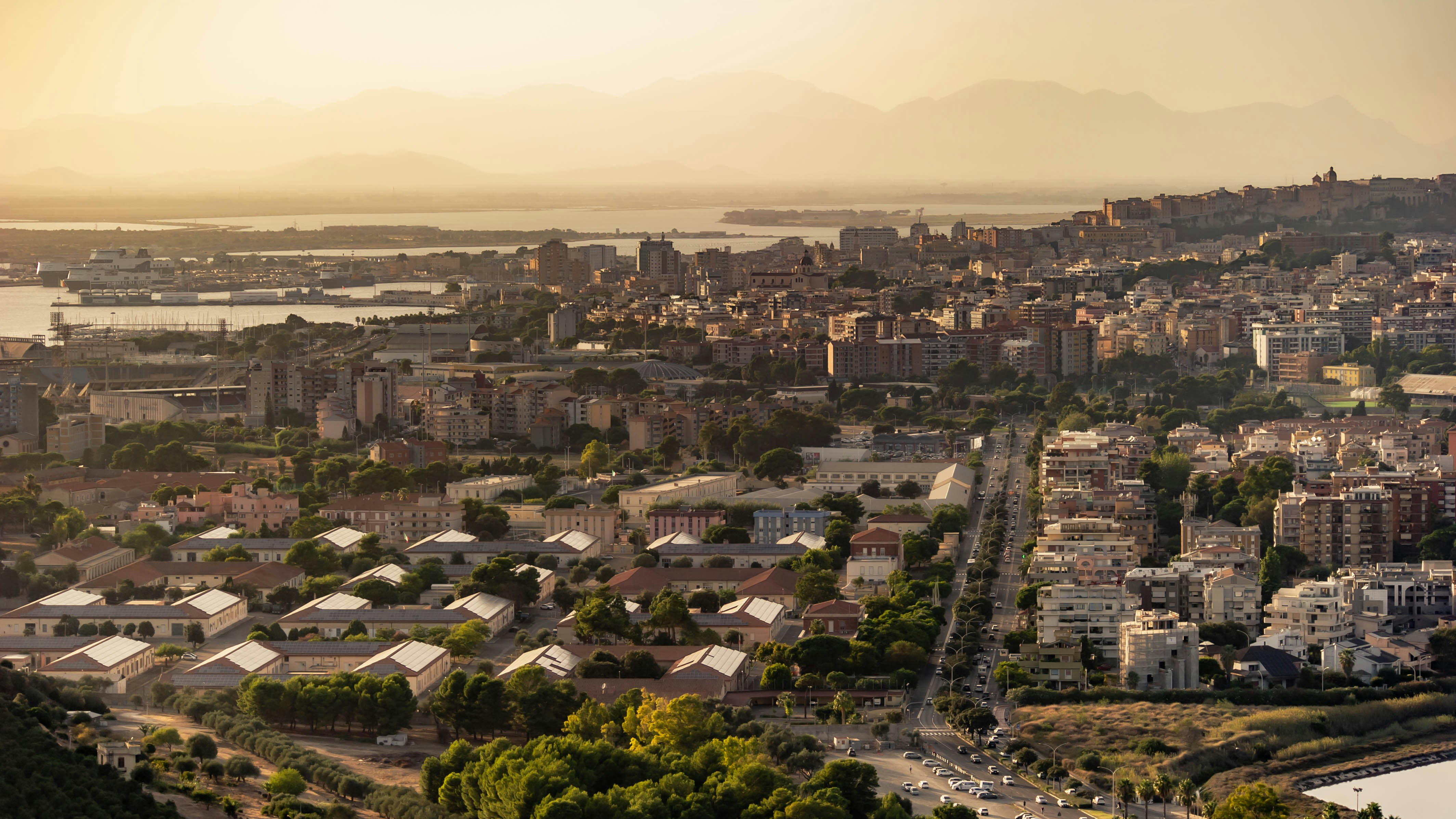 Cityscape at sunset with golden light illuminating buildings and distant mountains.