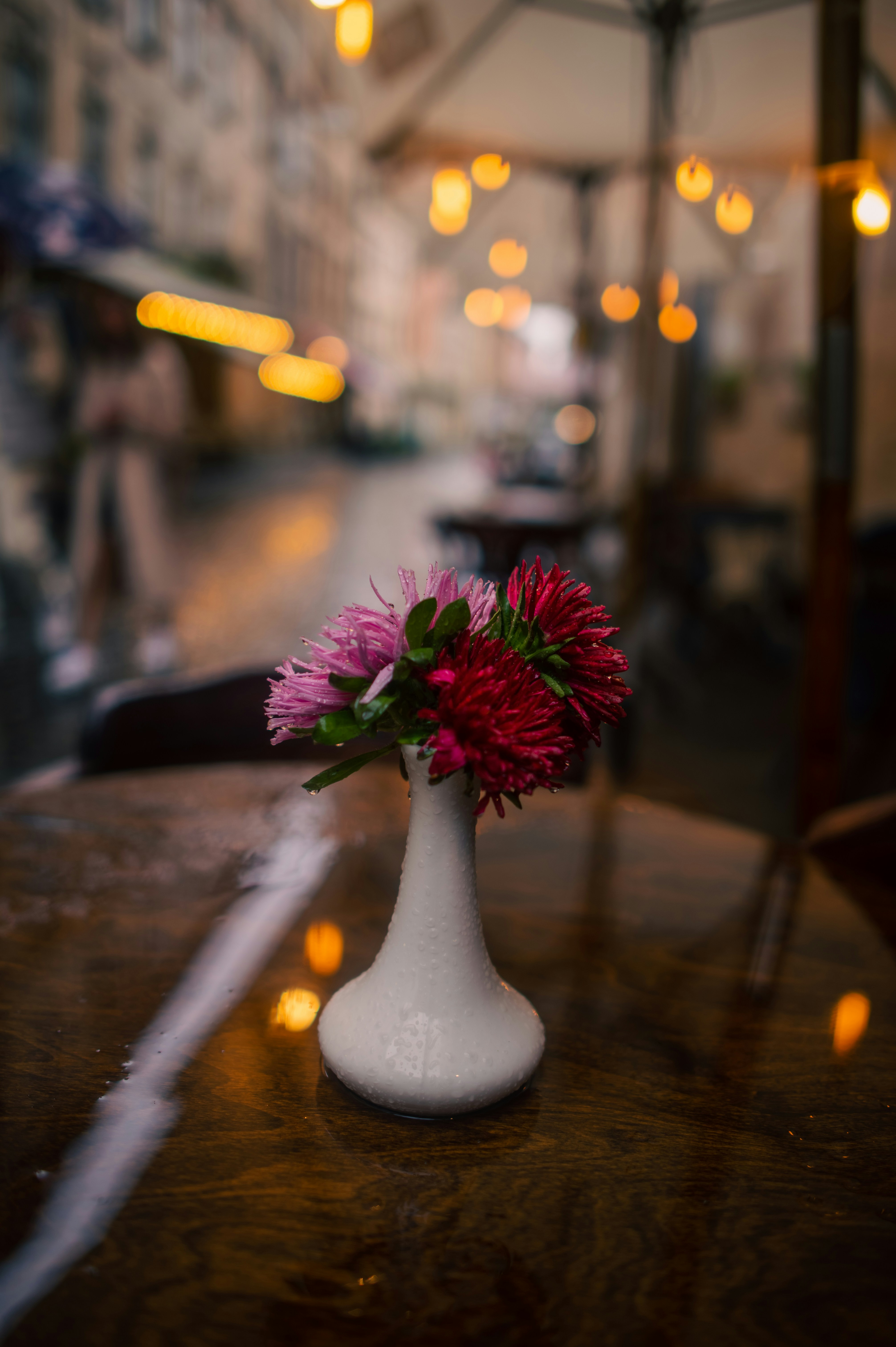 Soft Focus Bouquet: Pink and Magenta Blooms in a White Vase on a Glossy Café Table