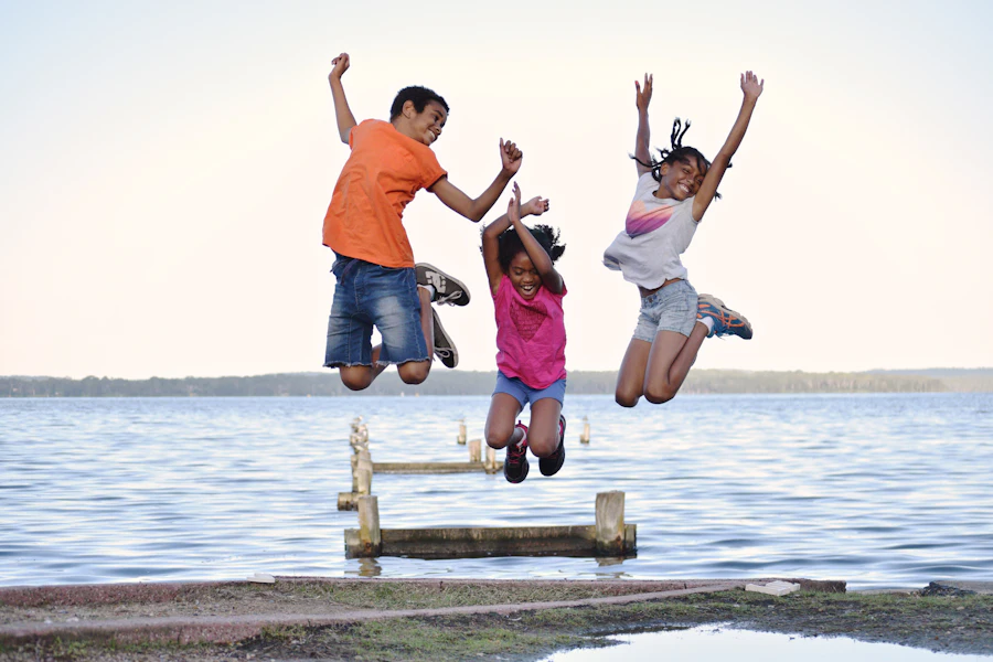 Three kids leap off a wooden dock into calm lake water, mid-air joy as the scene captures their energetic ascent at a sunny lakeside.