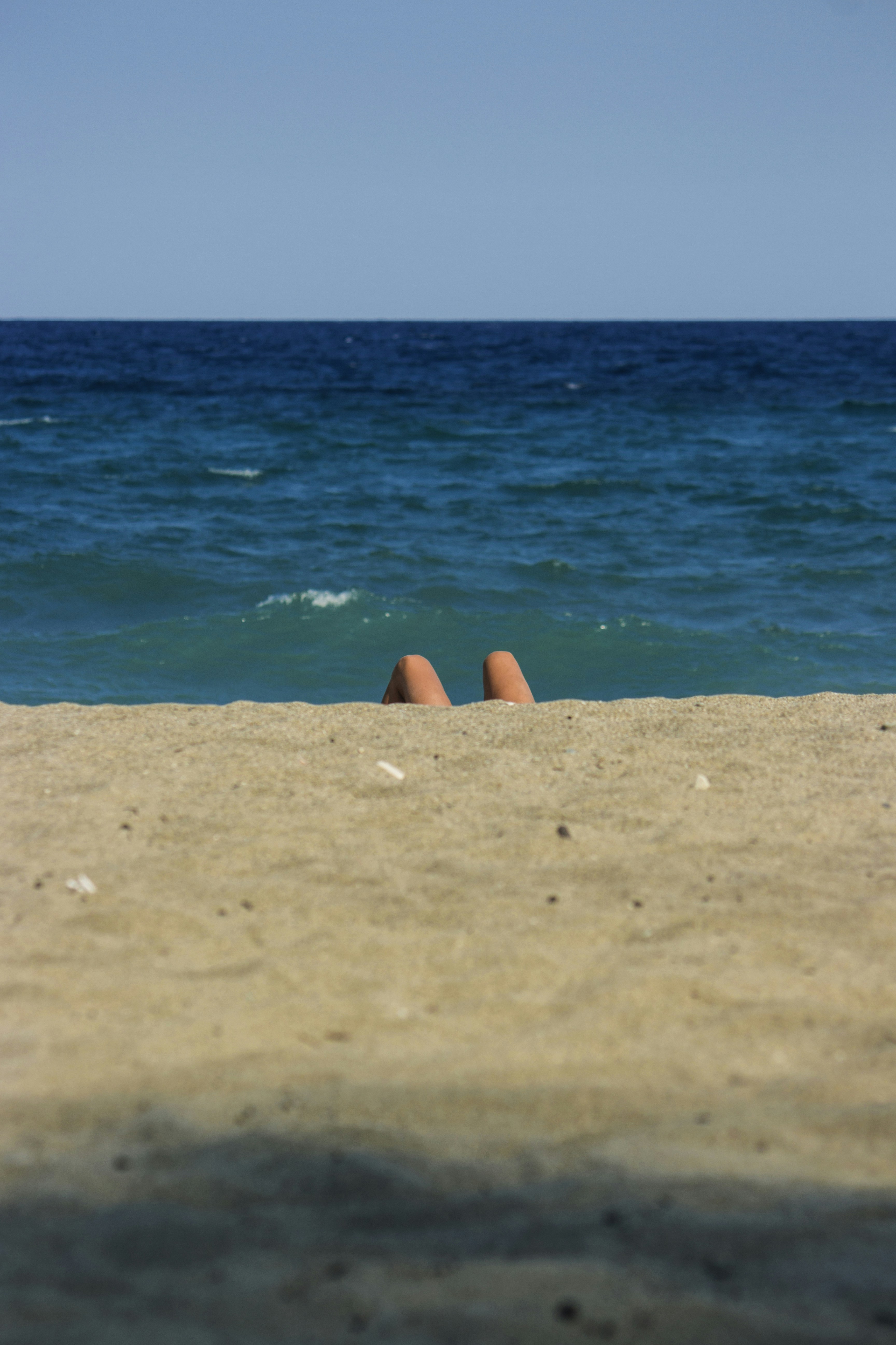 Dune Edge Pause: Legs Peeking Over Sand Toward a Quiet Sea