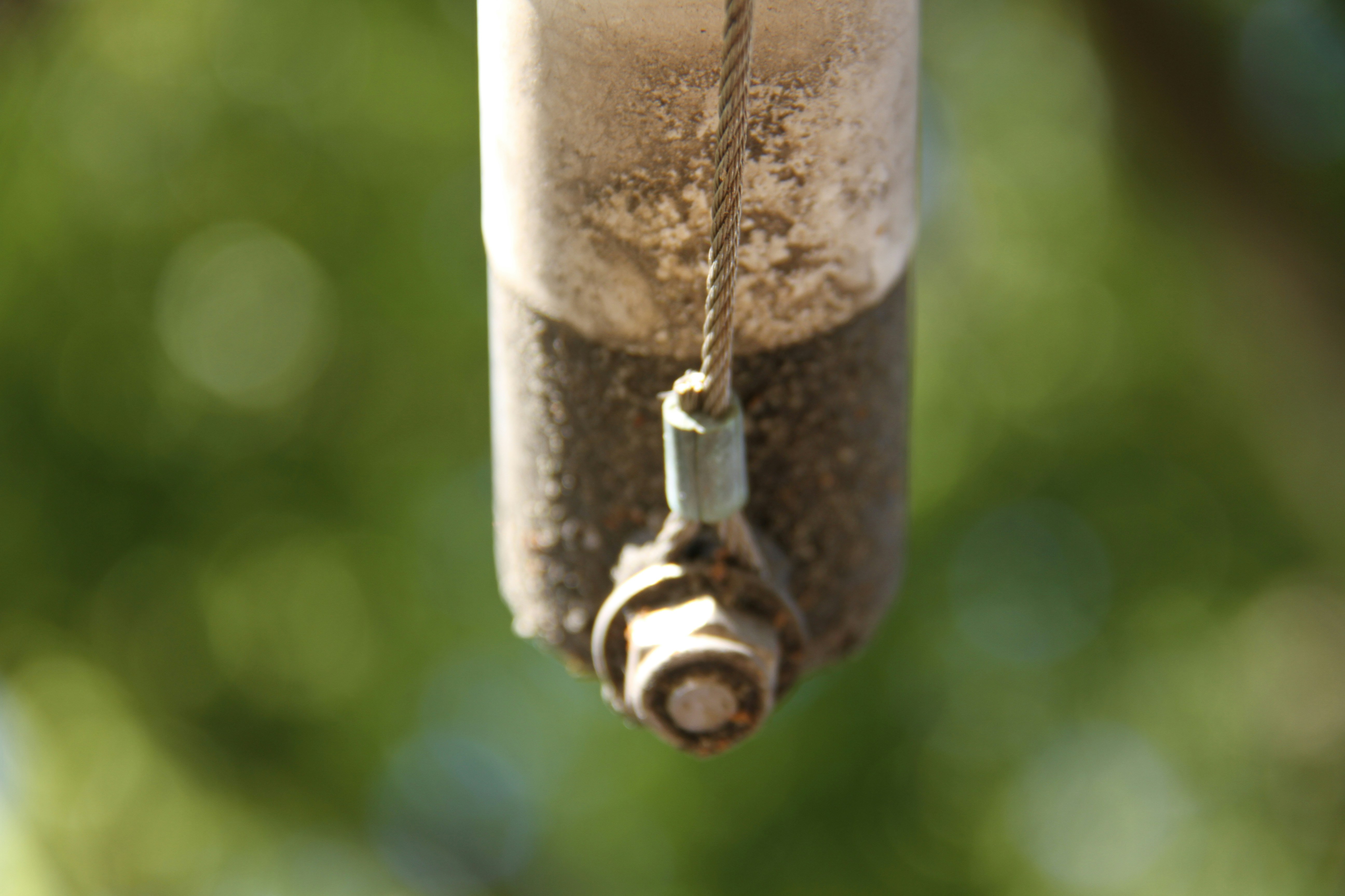 Close-up of a weathered pull mechanism and wire attached to a metal rod, with a blurred green background; the scene emphasizes the aged hardware and its rustic texture.