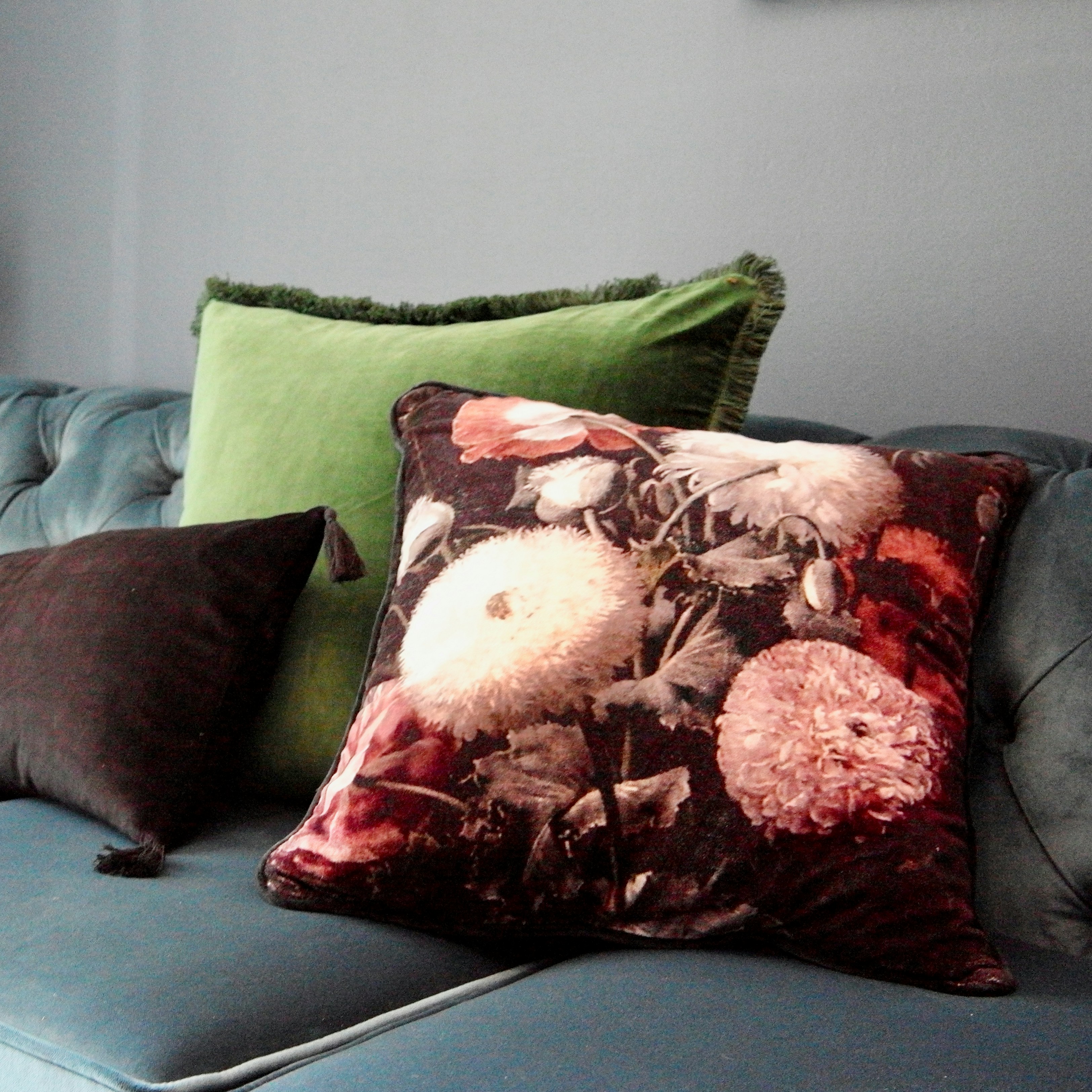 Photograph of a blue-gray sofa adorned with layered cushions, including a green back pillow and a vivid floral-patterned cushion.