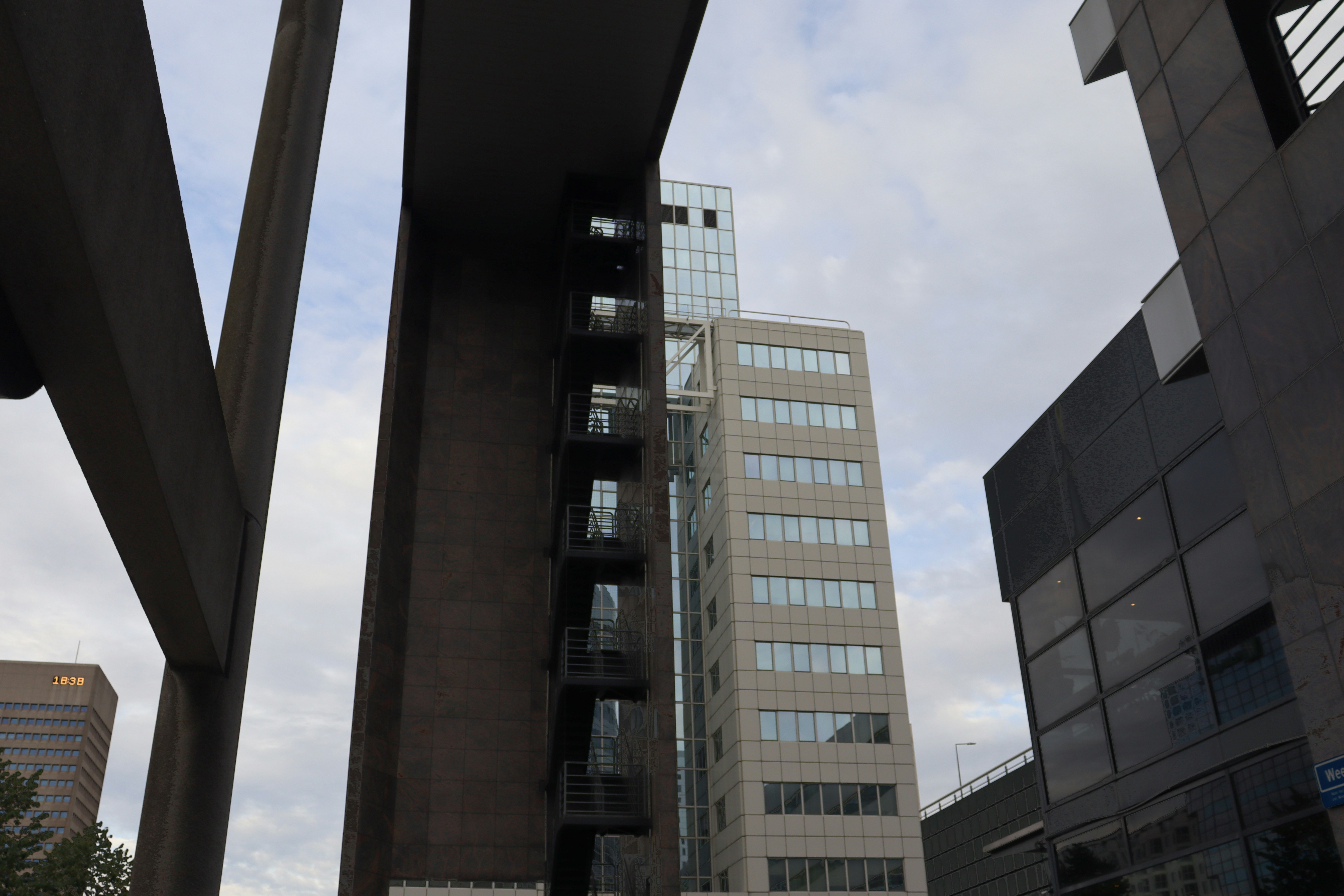 Modern skyscraper framed by angular architecture under a cloudy sky.