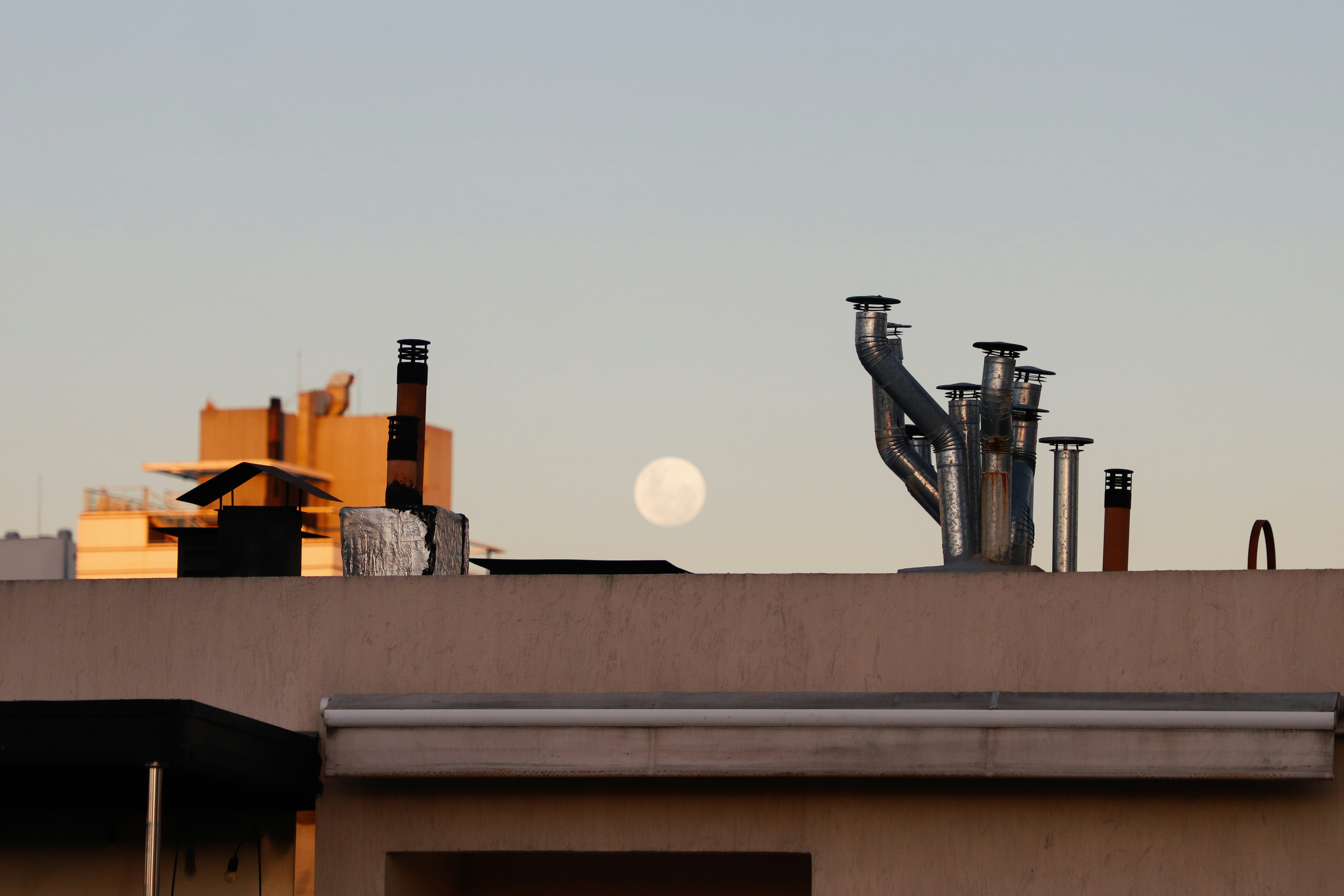 Full moon rising above rooftops, framed by industrial chimneys and urban architecture.