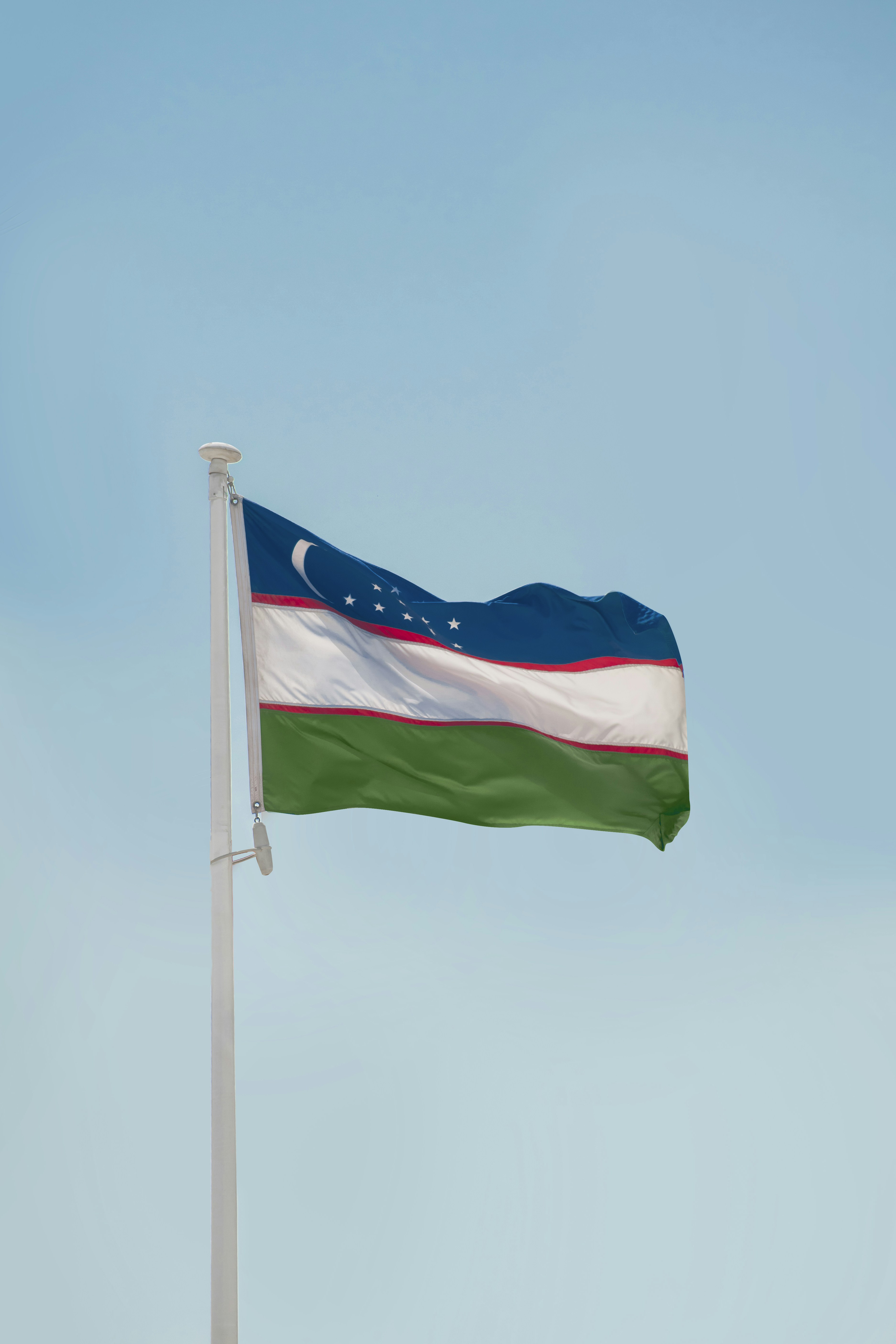 Uzbekistan's national flag billowing against a clear sky, showcasing its vibrant colors and distinct design.