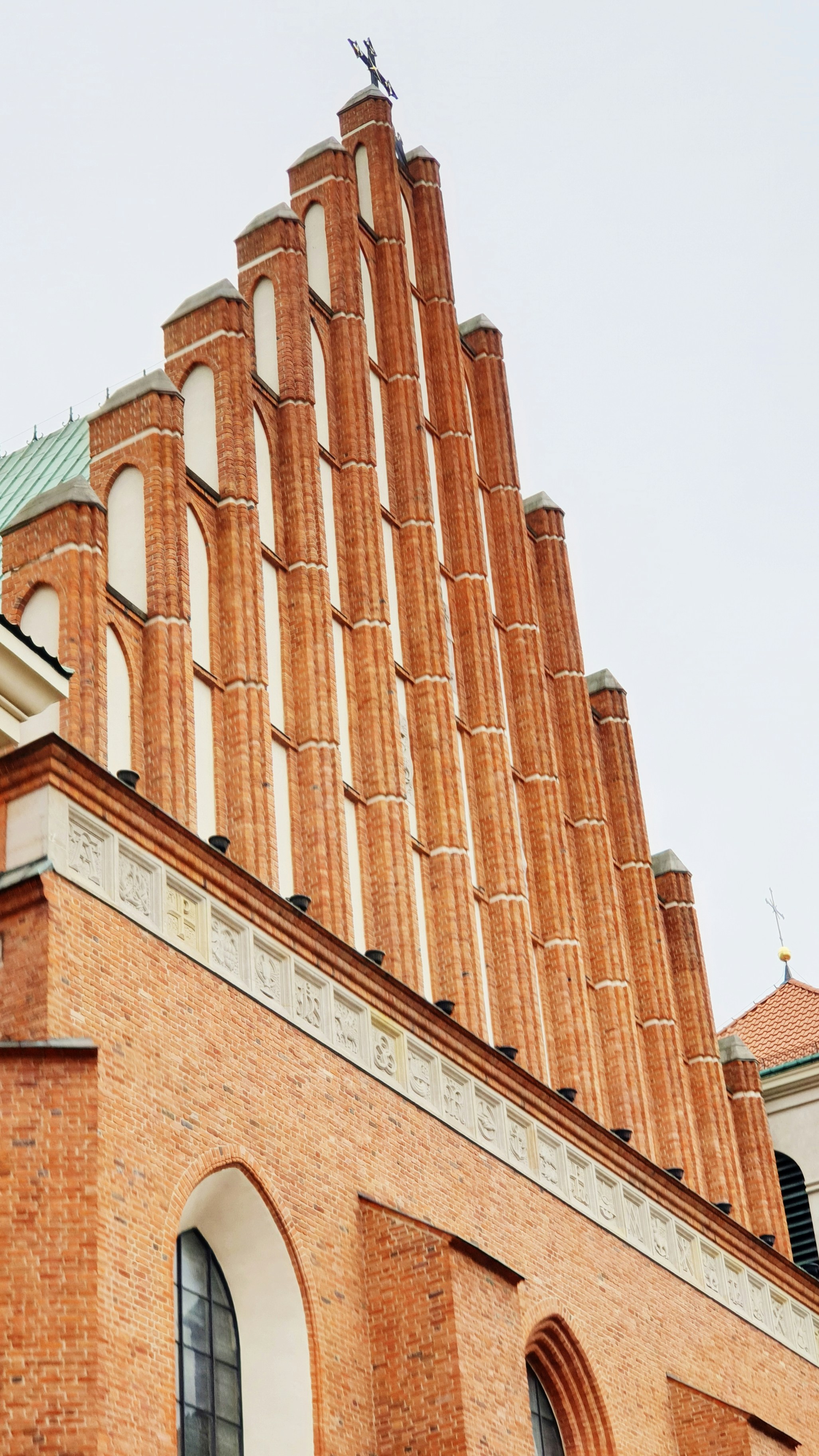 Intricate brickwork of a church facade showcasing a series of pointed arches and vertical lines, highlighted by a subtle sky backdrop.