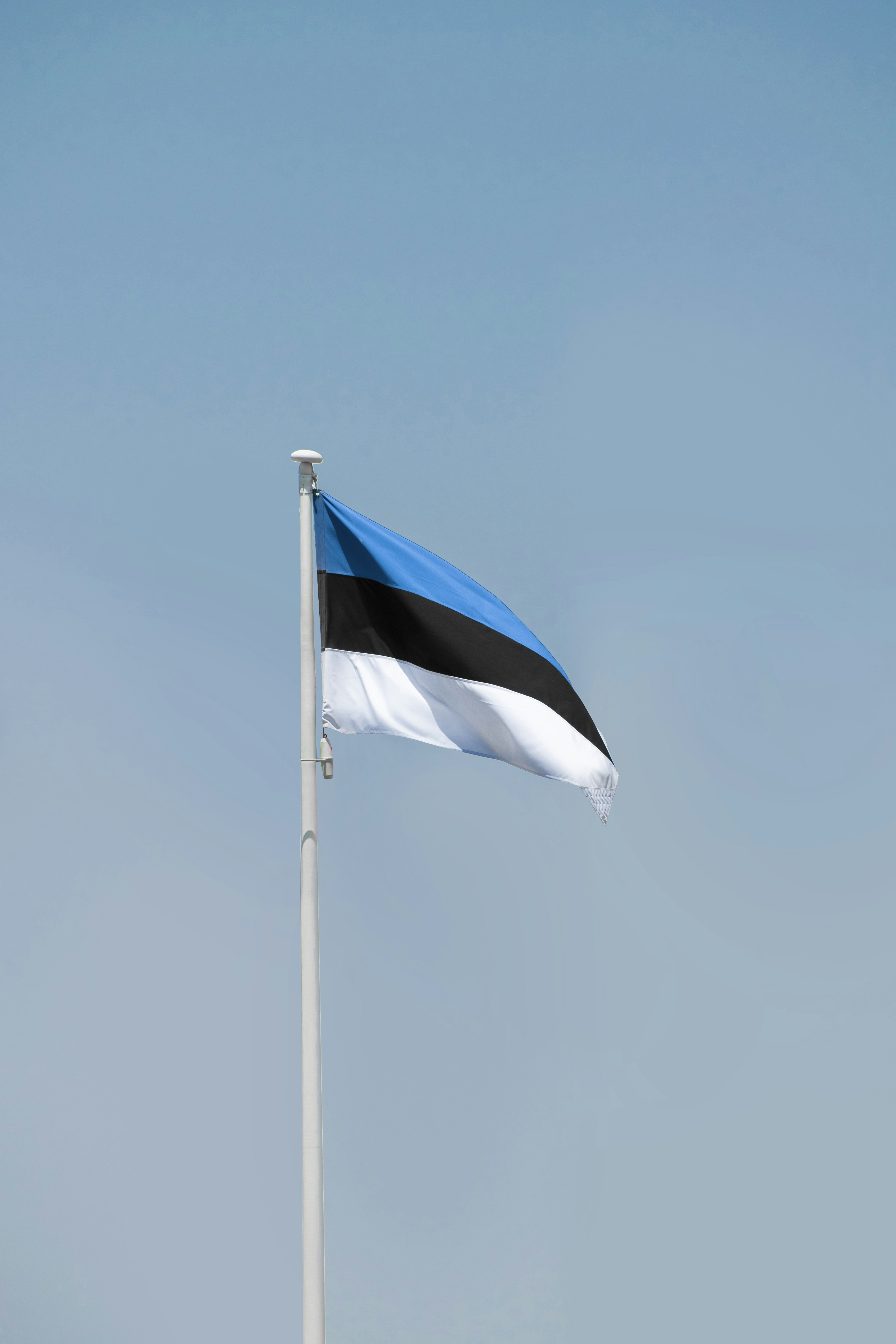 Estonian flag fluttering against a clear blue sky, showcasing its distinctive black, blue, and white stripes.