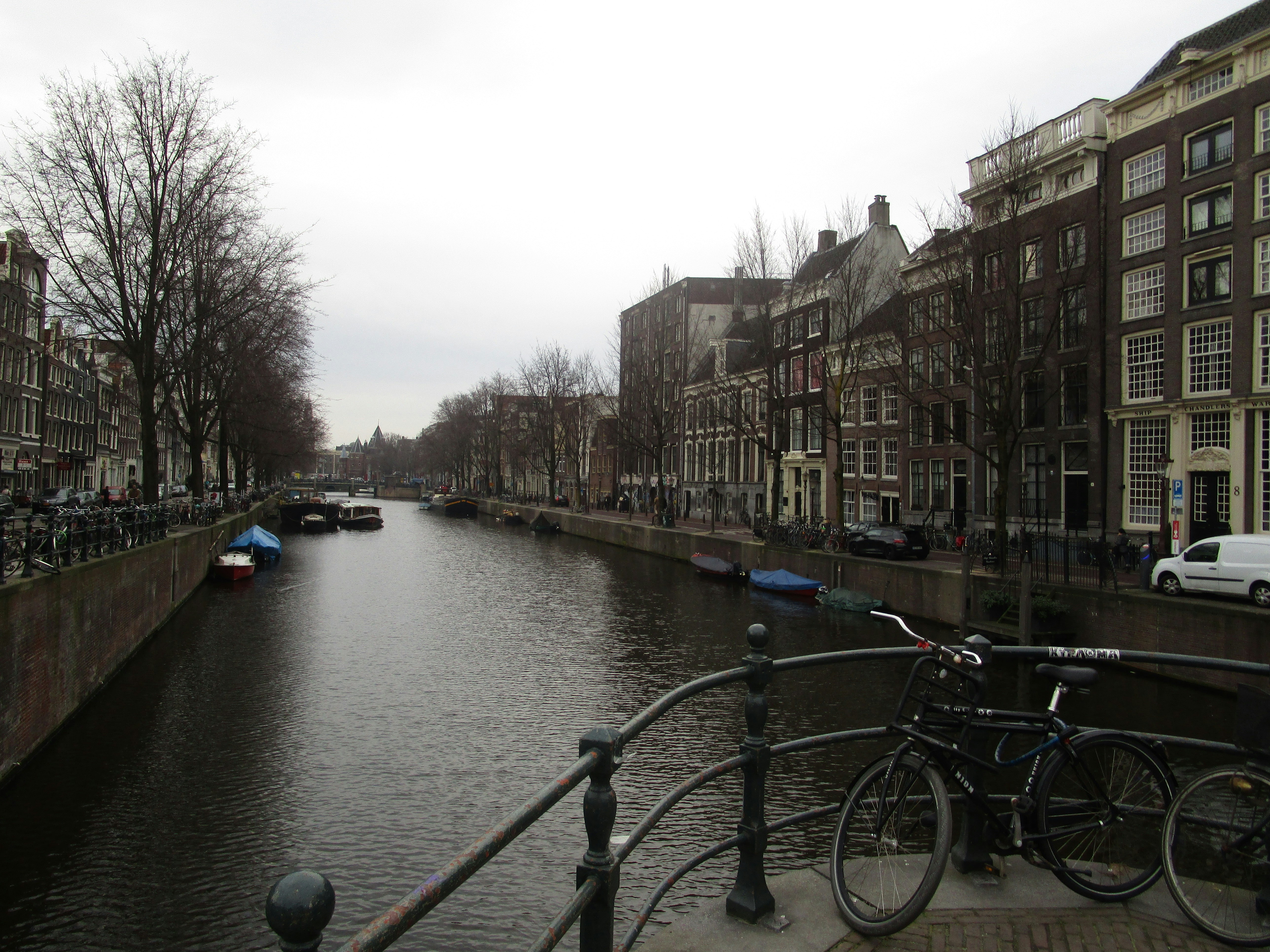 Canal scene in Amsterdam featuring historic buildings and moored boats, with a bicycle on the foreground railing.