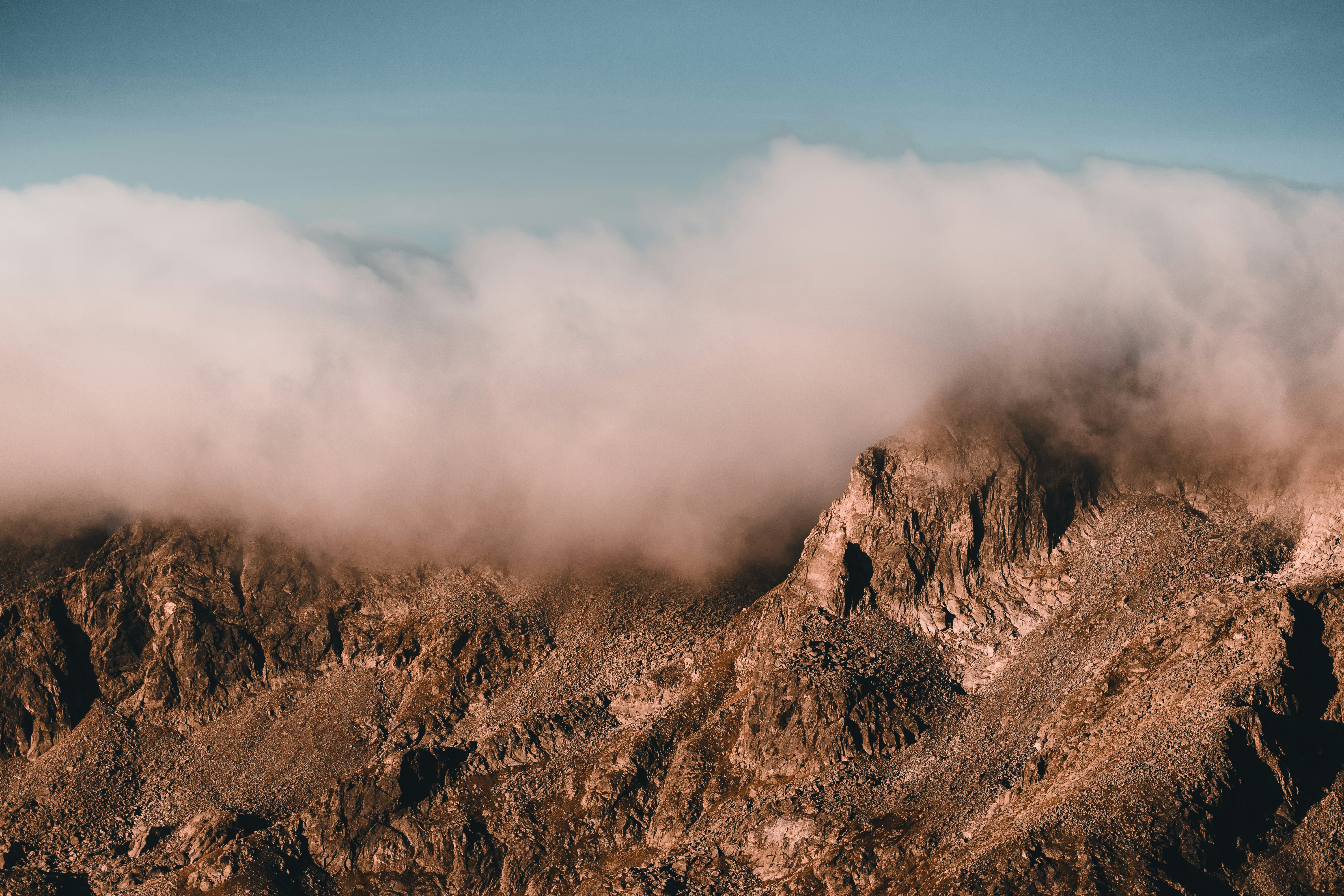 Clouds gently envelop jagged mountain peaks under a clear sky.