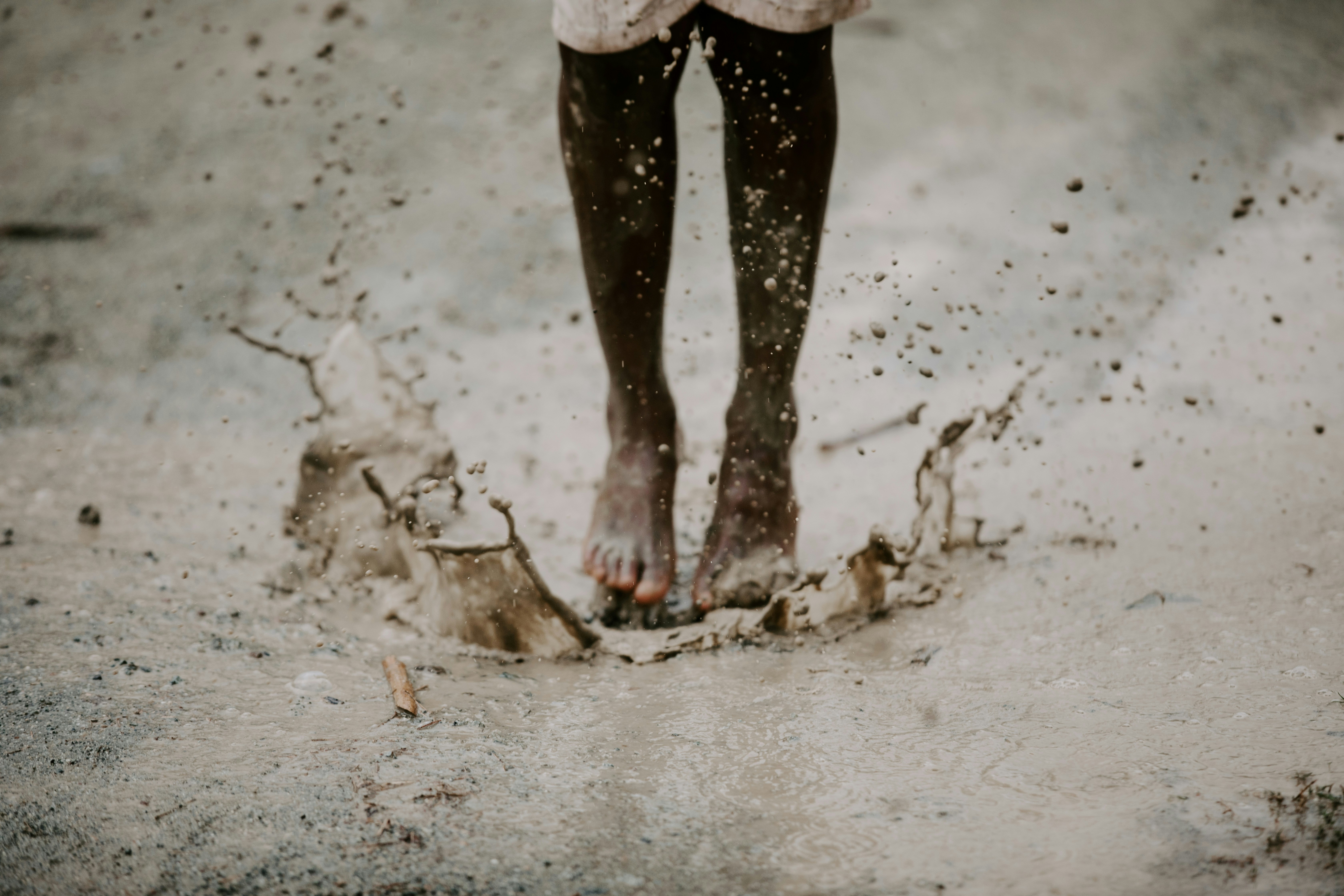 Child's bare feet splashing in muddy water, sending droplets into the air. The moment captures the essence of playful exploration.