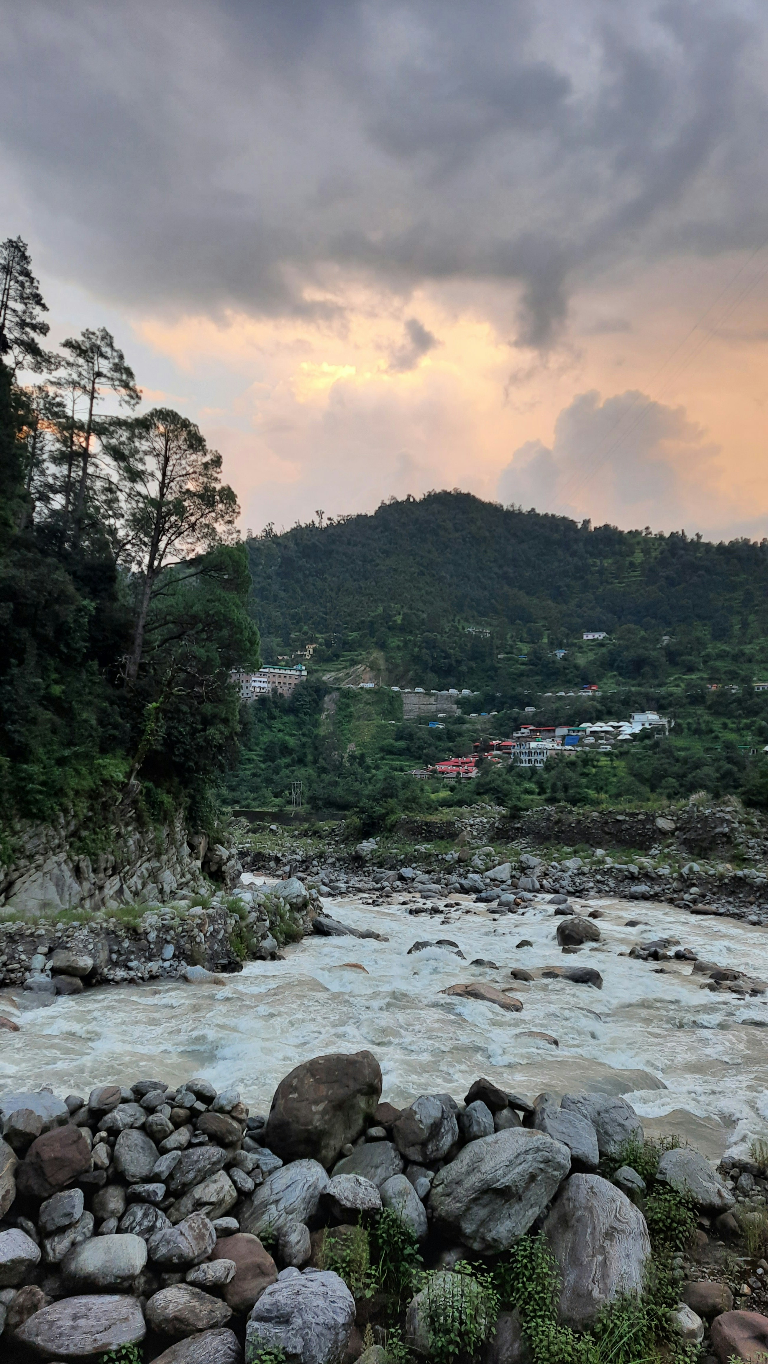 Rushing river with rocky banks beneath a cloudy evening sky and distant hills.