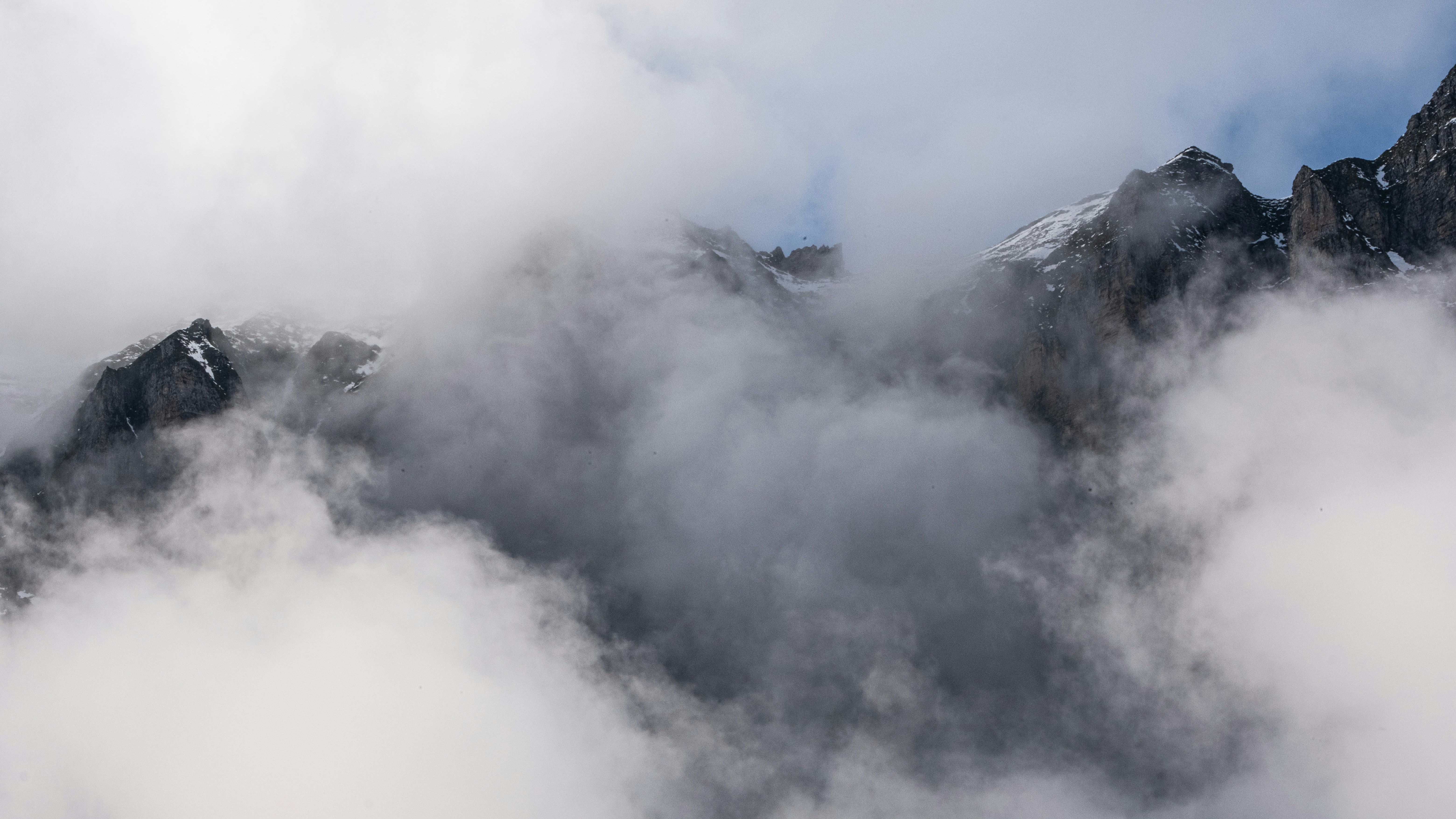 Misty mountain landscape shrouded in clouds, revealing rocky peaks dusted with snow. A serene atmosphere envelops the scene.