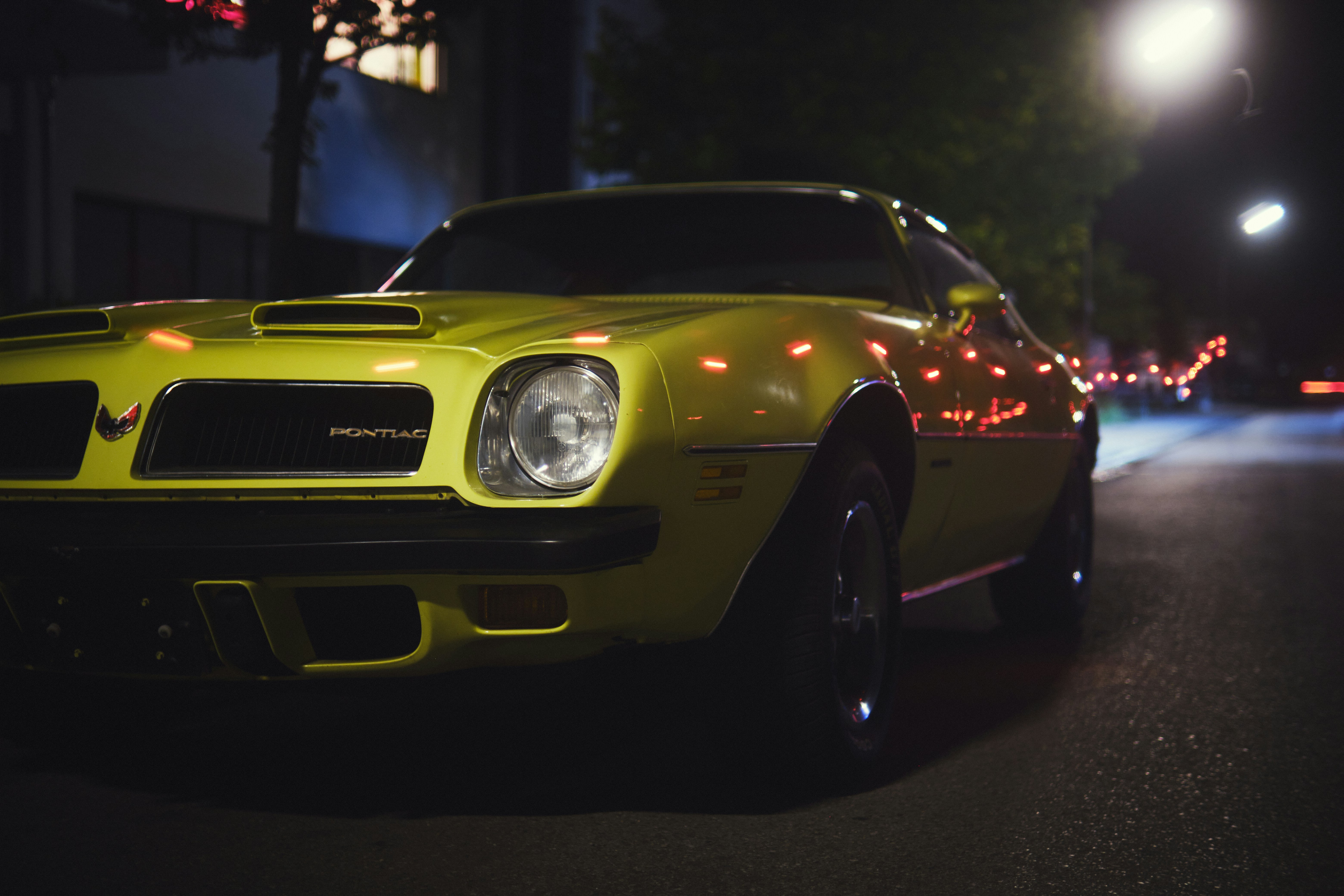 Neon-Glow Muscle: Yellow Pontiac Firebird tucked under city-night streetlights