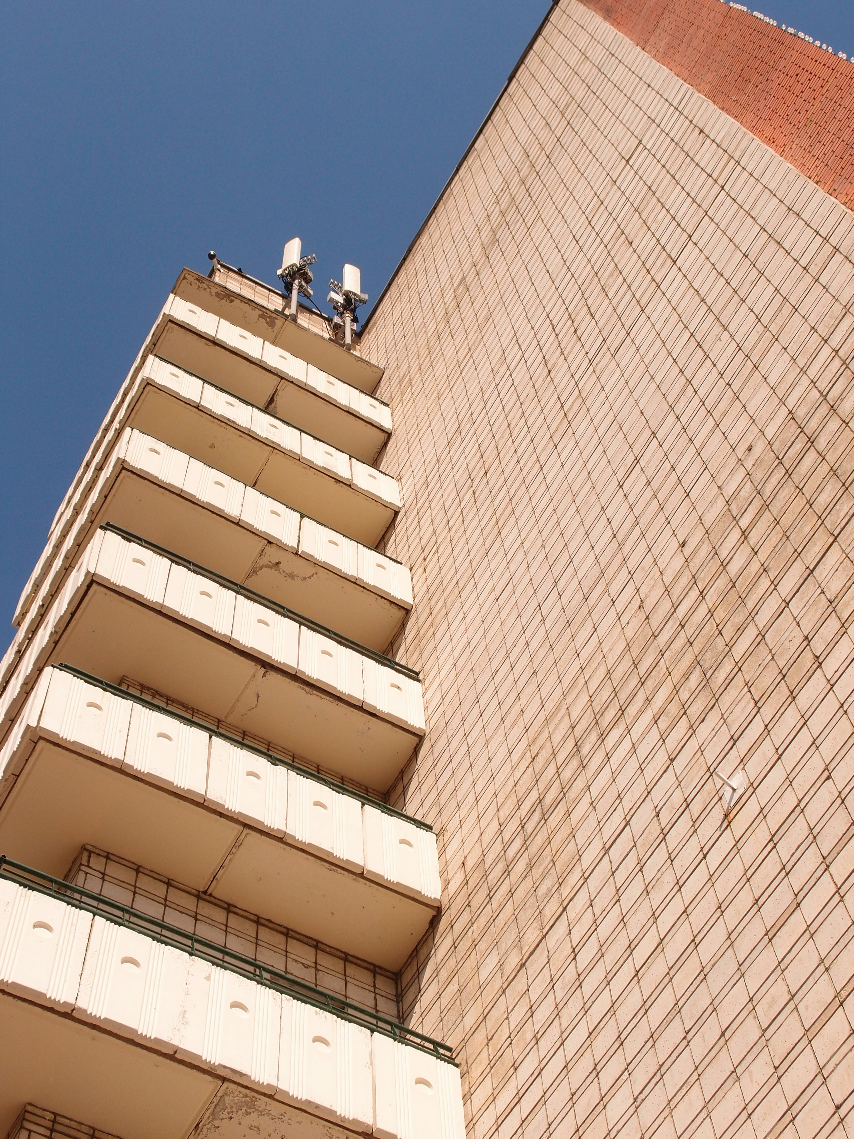 A close-up view of a high-rise building's balconies and antennas against a clear blue sky. The geometric patterns and textures create an intriguing urban aesthetic.