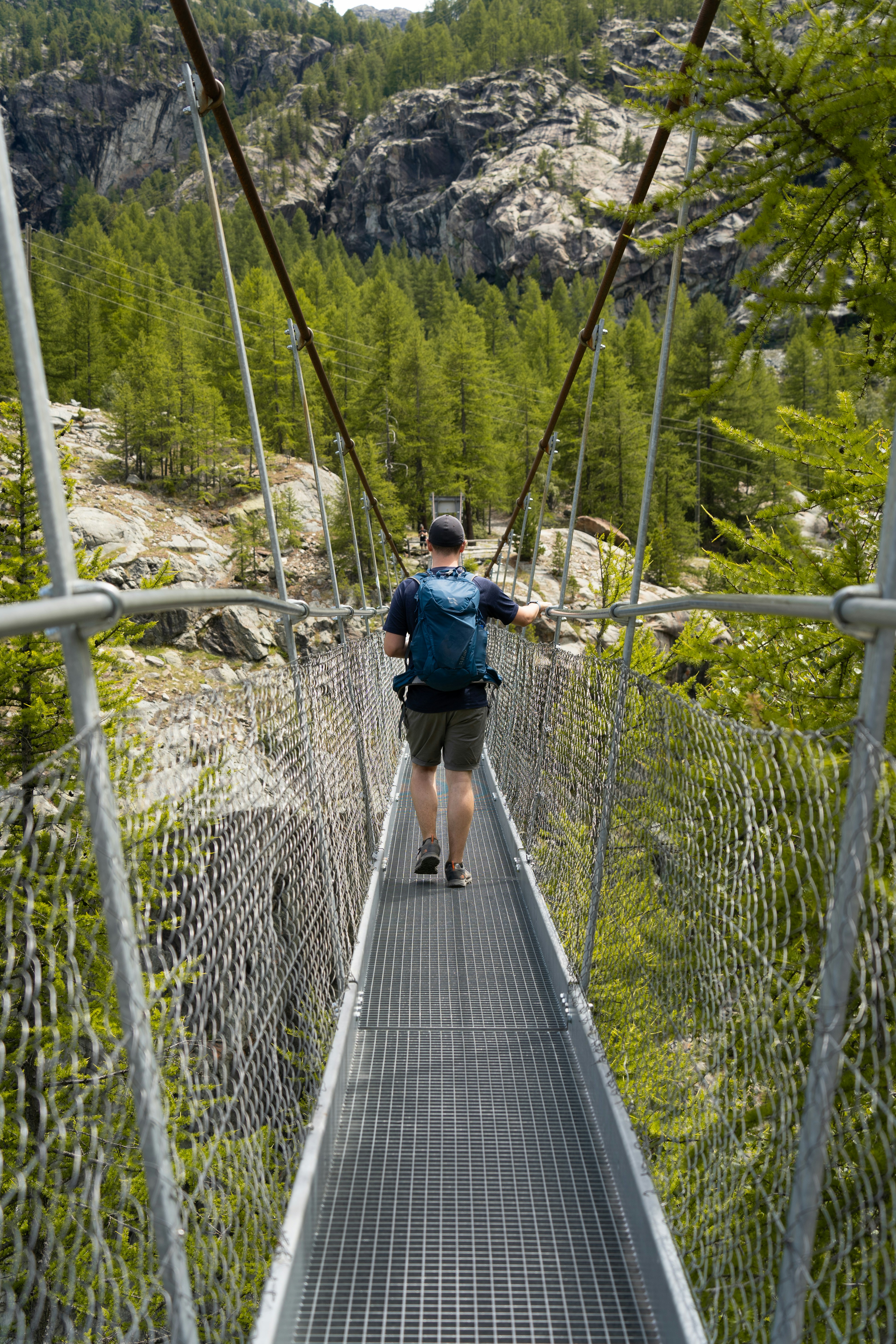 A hiker traverses a suspension bridge surrounded by lush greenery and rugged cliffs, illustrating the thrill of exploration in nature.