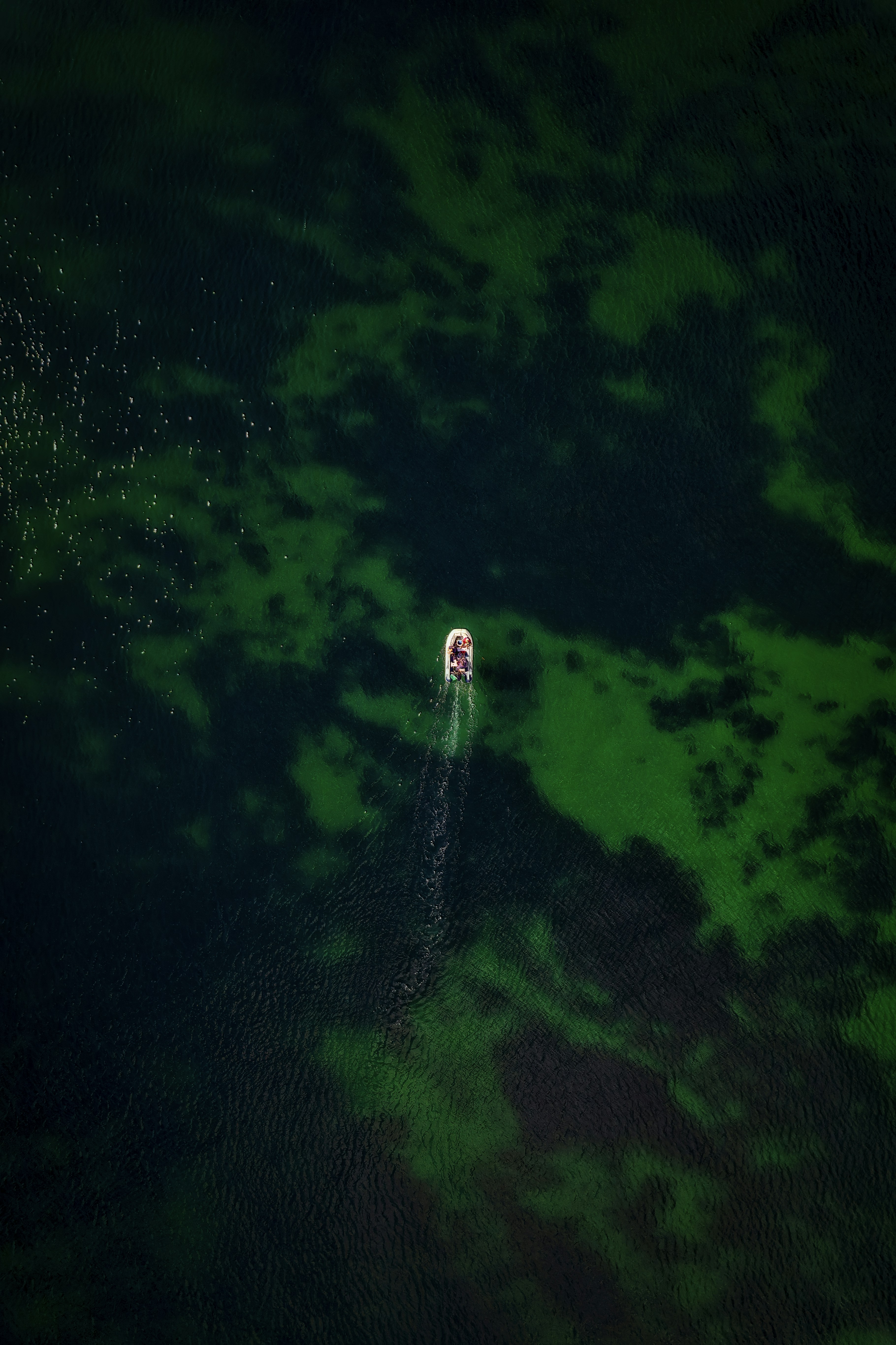 Green Peace. An isolated boat of anglers glides through the green and aqua sea of the Jurassic Coast, UK.