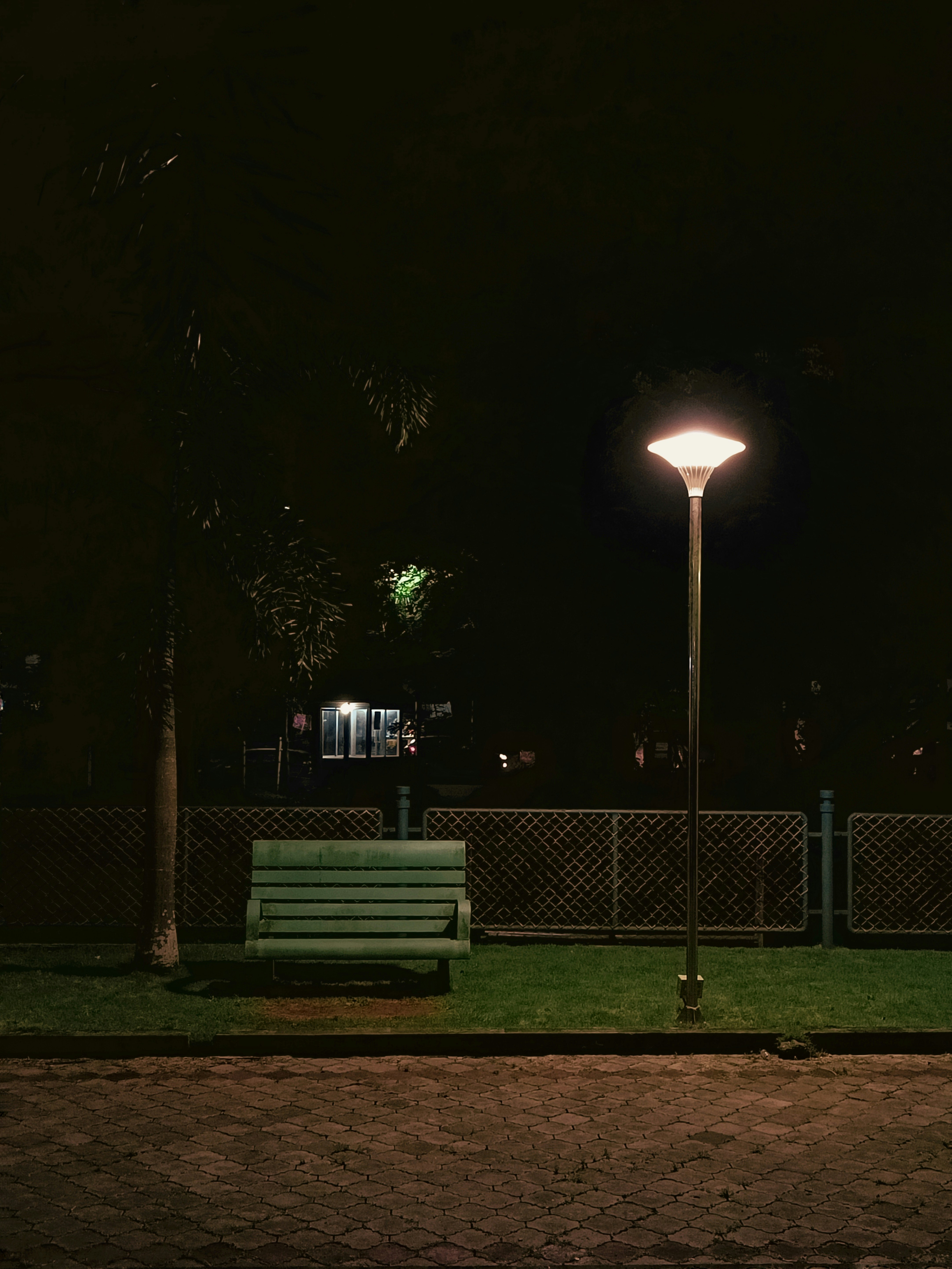 Green bench in a park at night, under garden light. | a bench sits unoccupied