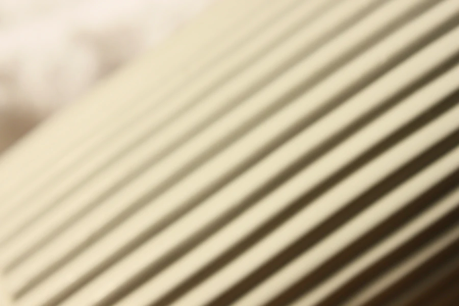 Close-up of a cream-colored ribbed surface with strong diagonal lines and shallow depth of field. Soft warm highlights fade into shadow along the lower edge.