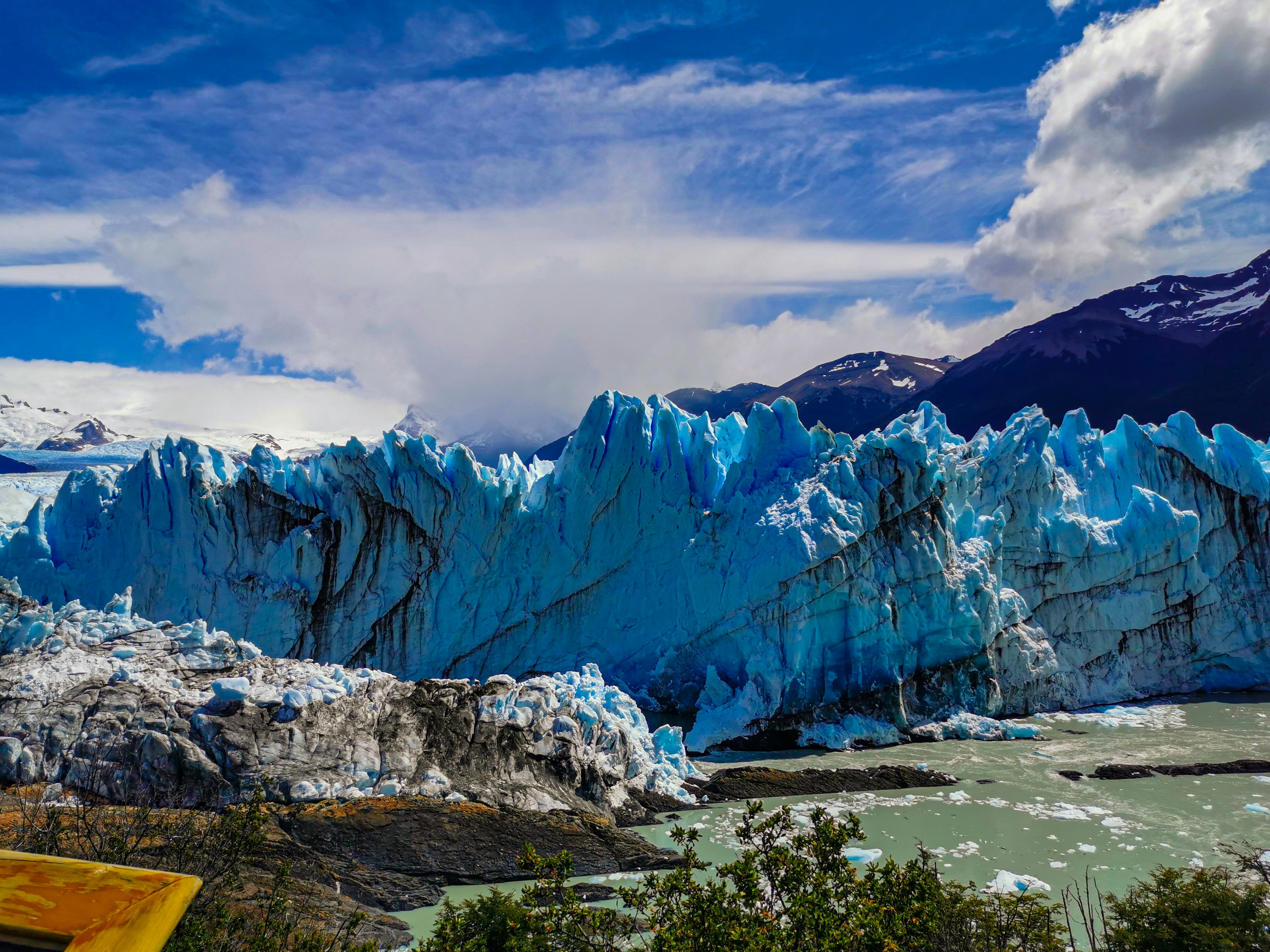 Massive glacier formations tower against a backdrop of mountains and blue skies, reflecting the dynamic beauty of nature's ice sculptures.