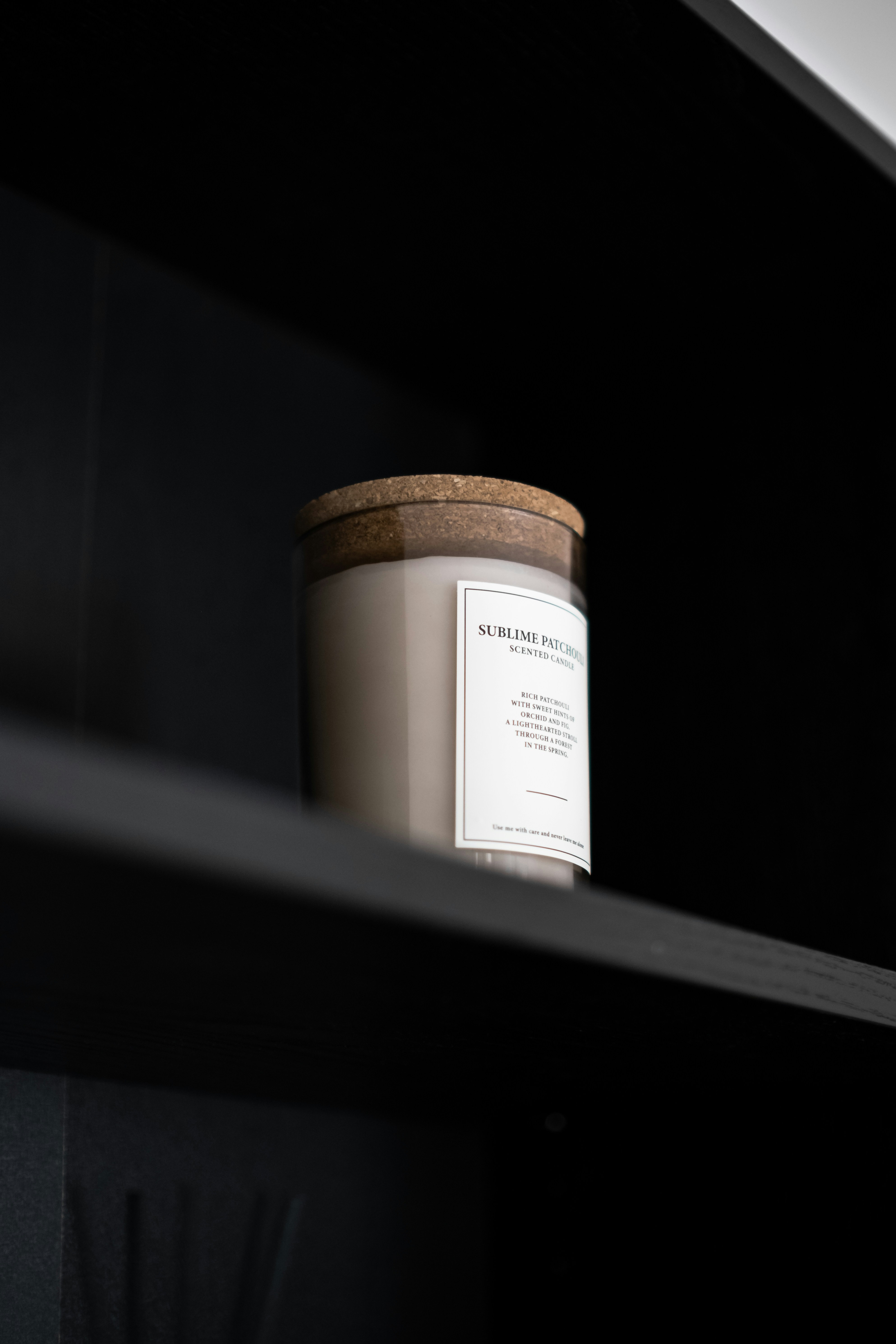 Candle with a cork lid labeled 'Sublime Patchouli' resting on a dark shelf, highlighting minimalist design and ambiance.