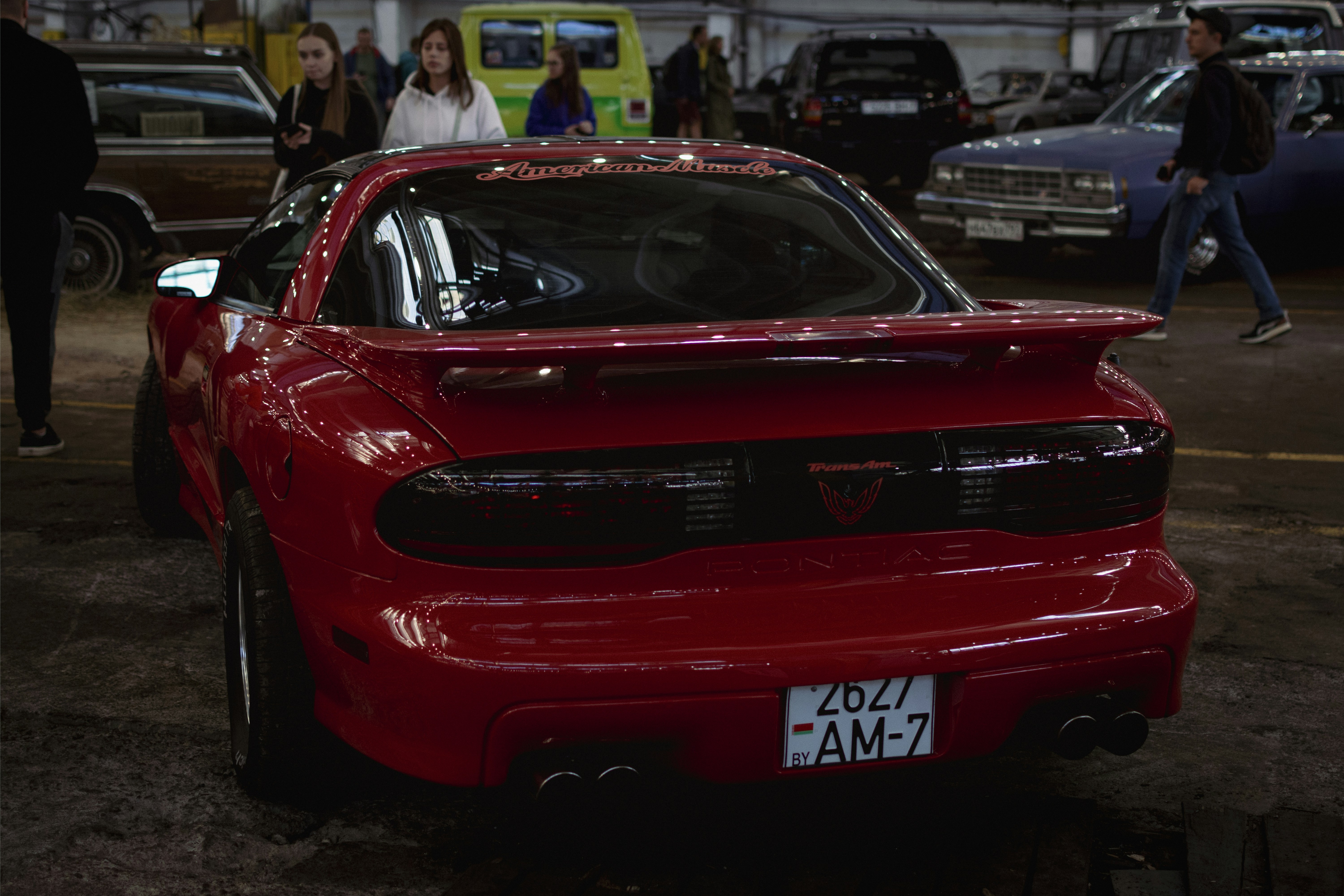 A red sports car parked in a parking lot with people walking around ...