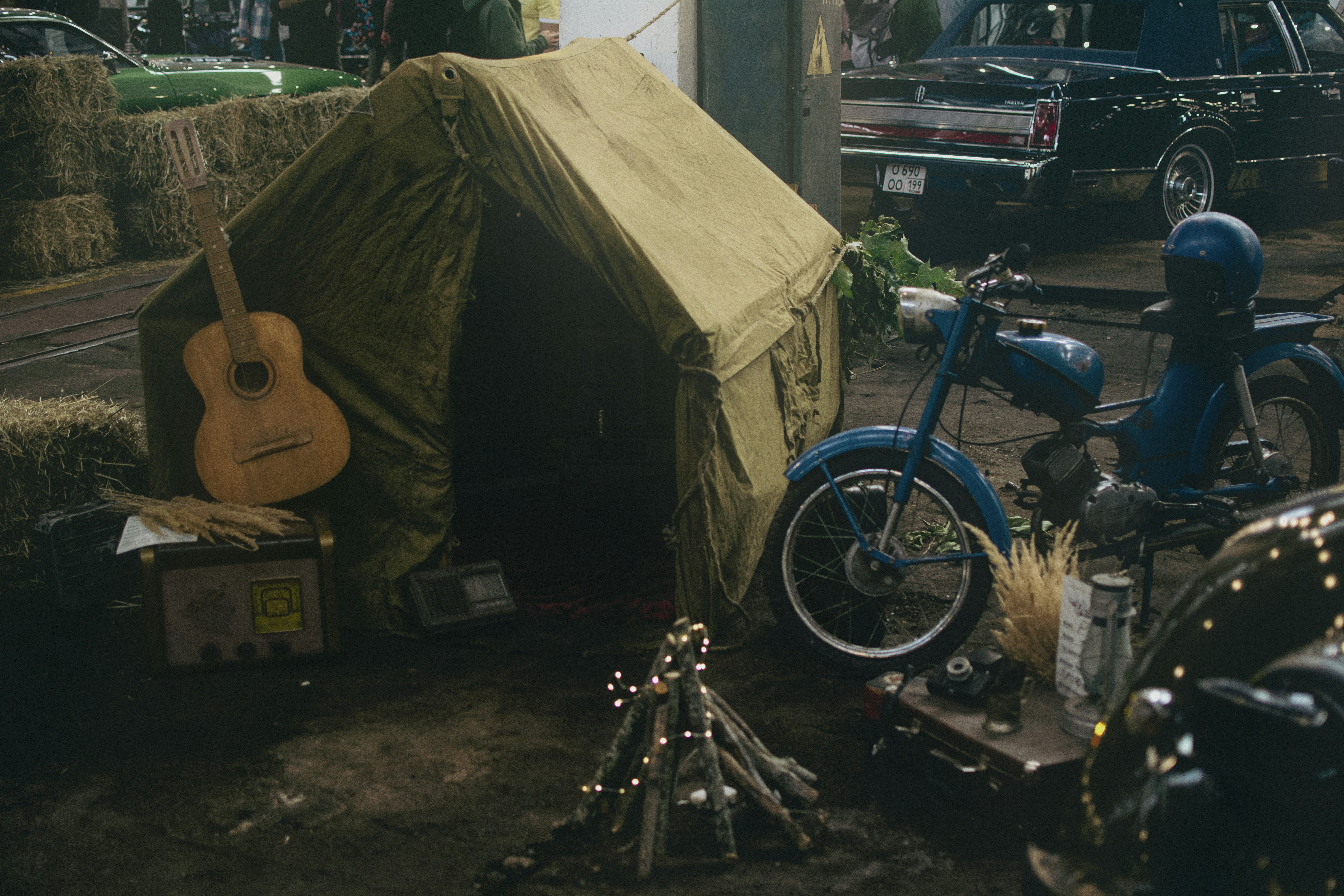 Urban Campout: Tent, Guitar, and Retro Ride Amid Dim Neon Glow
