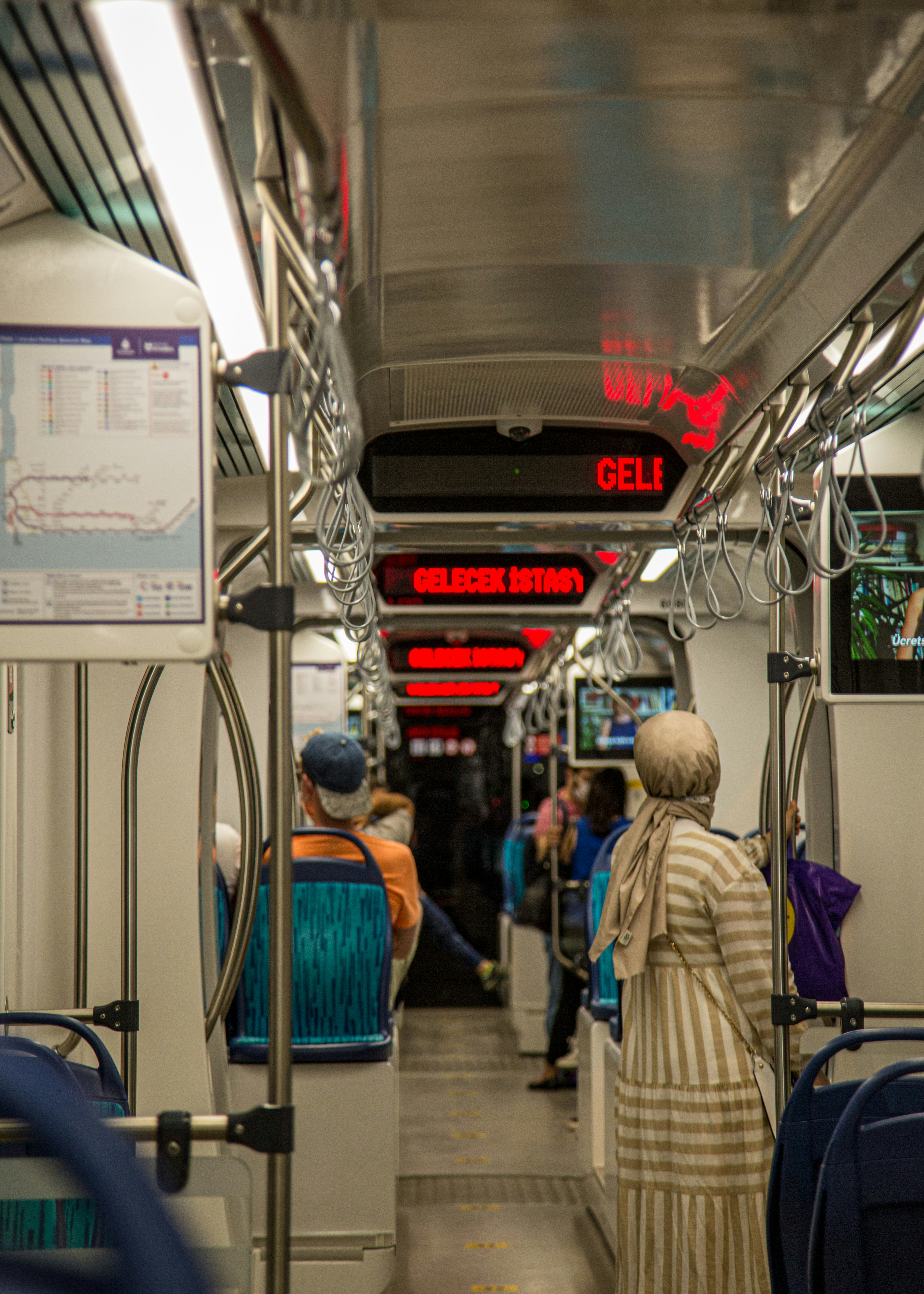 Interior view of a public transport vehicle featuring illuminated station signs and passengers seated along the aisle.