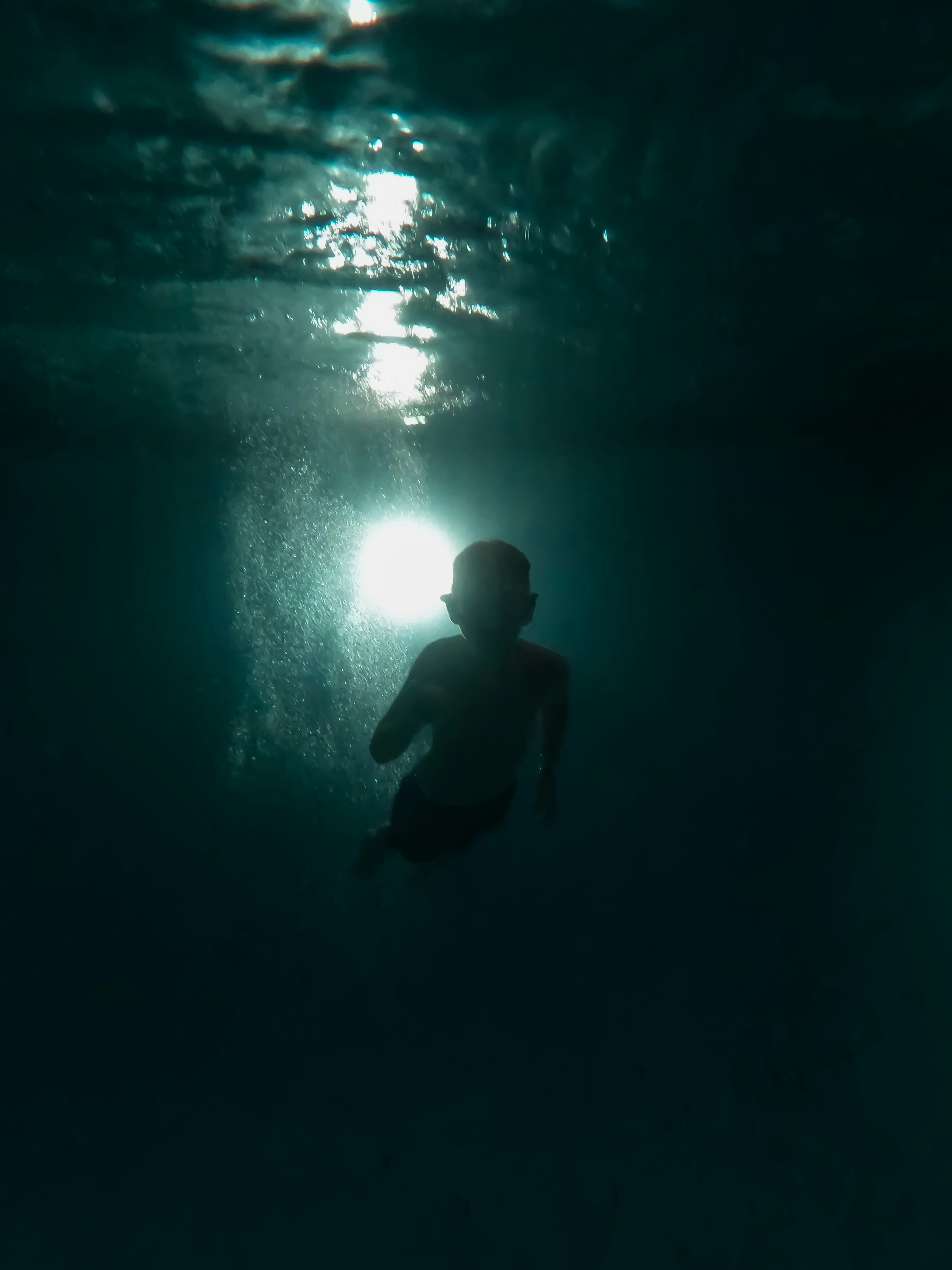 Sunlit Underwater Silhouette: A Lone Swimmer in Teal Depths