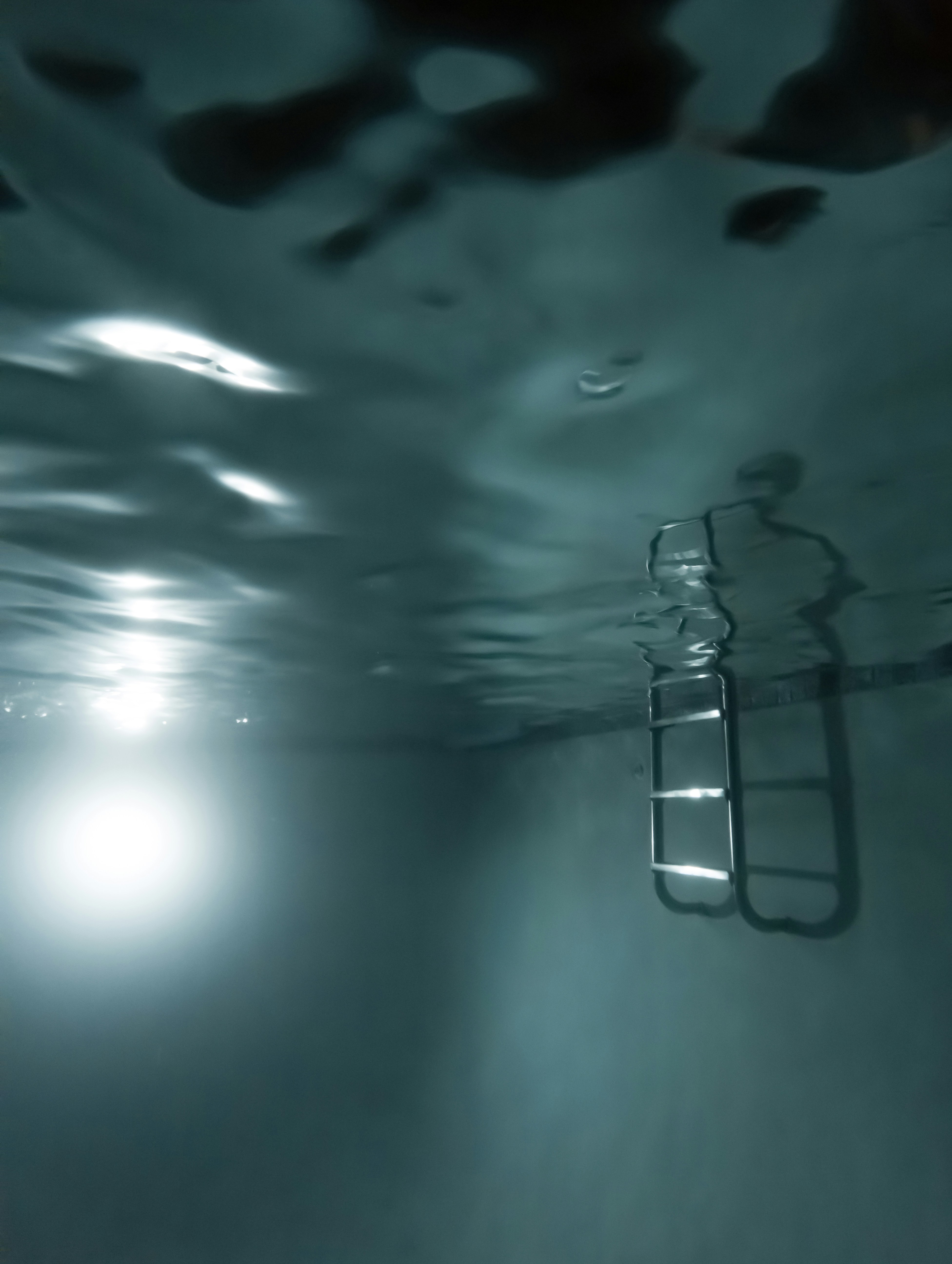 Underwater view showcasing a metallic ladder illuminated by soft light, creating a serene atmosphere in a pool.