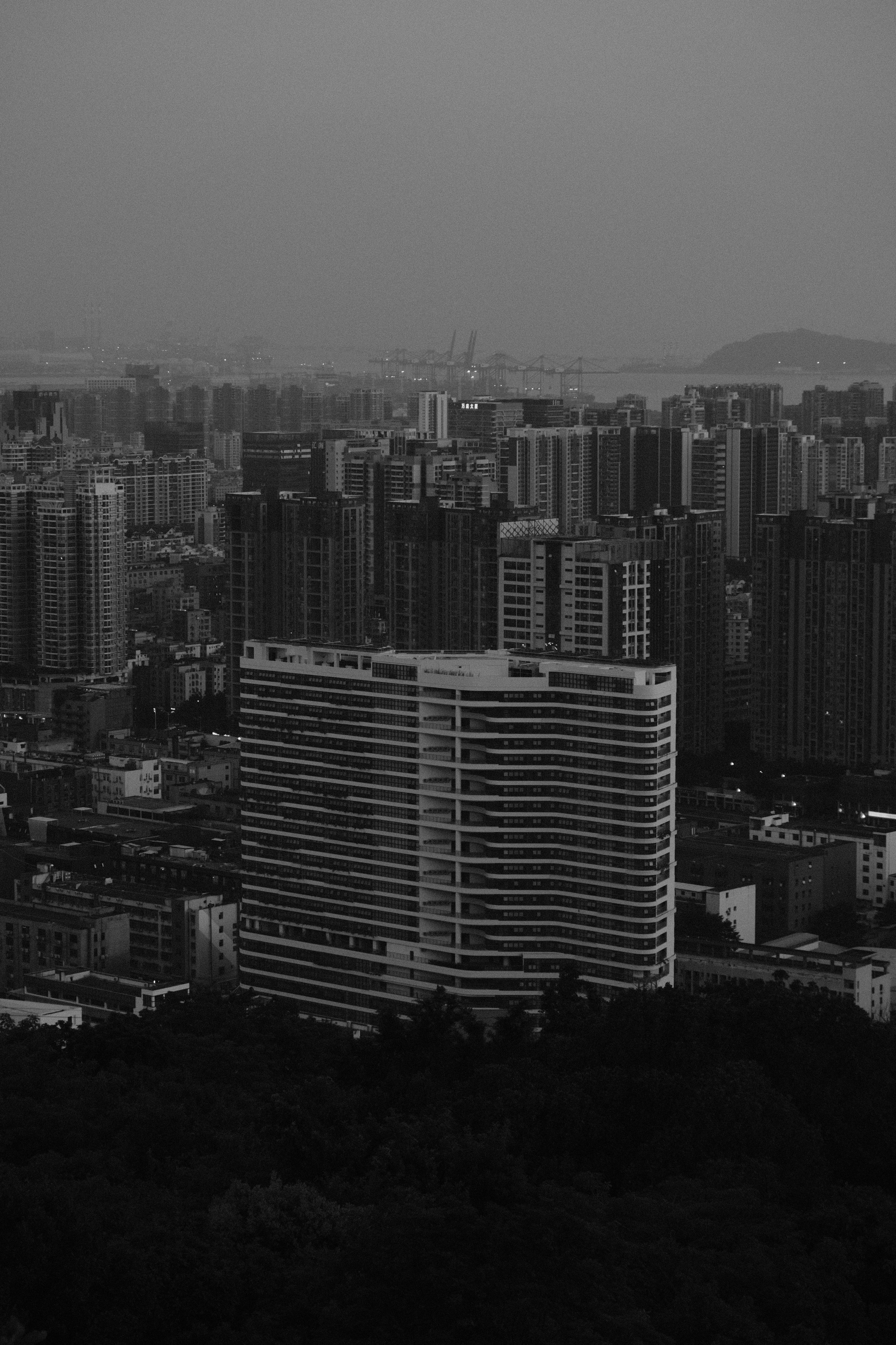 High-rise buildings loom over a modern architectural structure, creating a stark contrast in this black-and-white cityscape.
