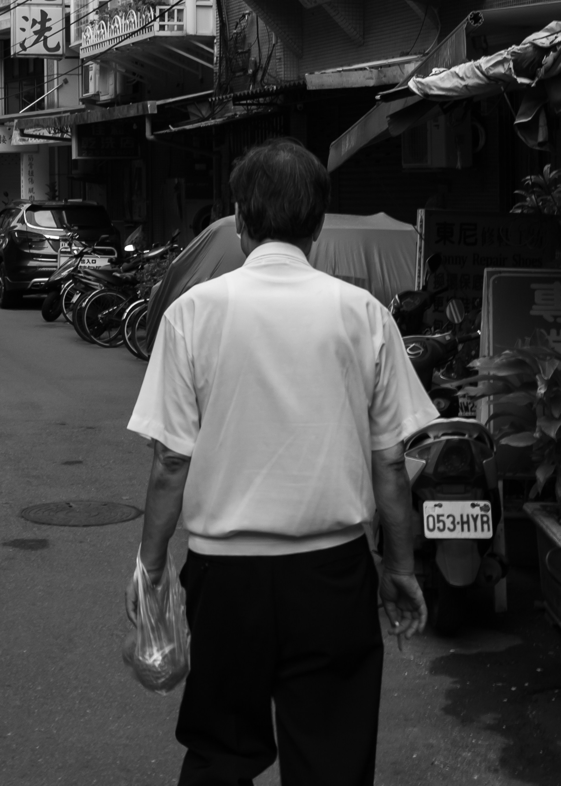 Elderly man walking down a bustling street, carrying a bag, surrounded by parked bicycles and market stalls.