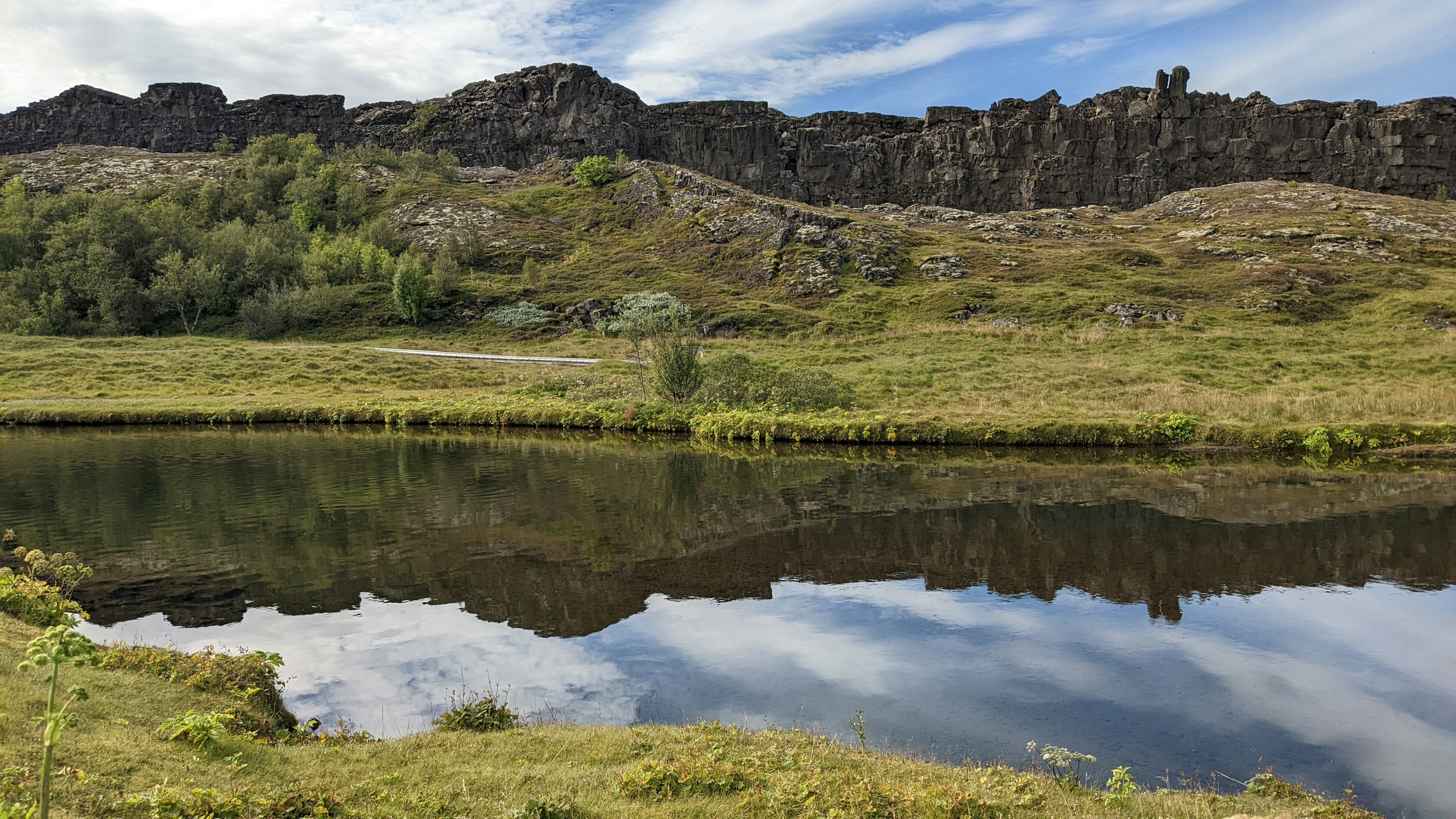 A serene landscape featuring a calm body of water reflecting rugged cliffs and lush greenery. Ideal for showcasing the harmony between land and water.