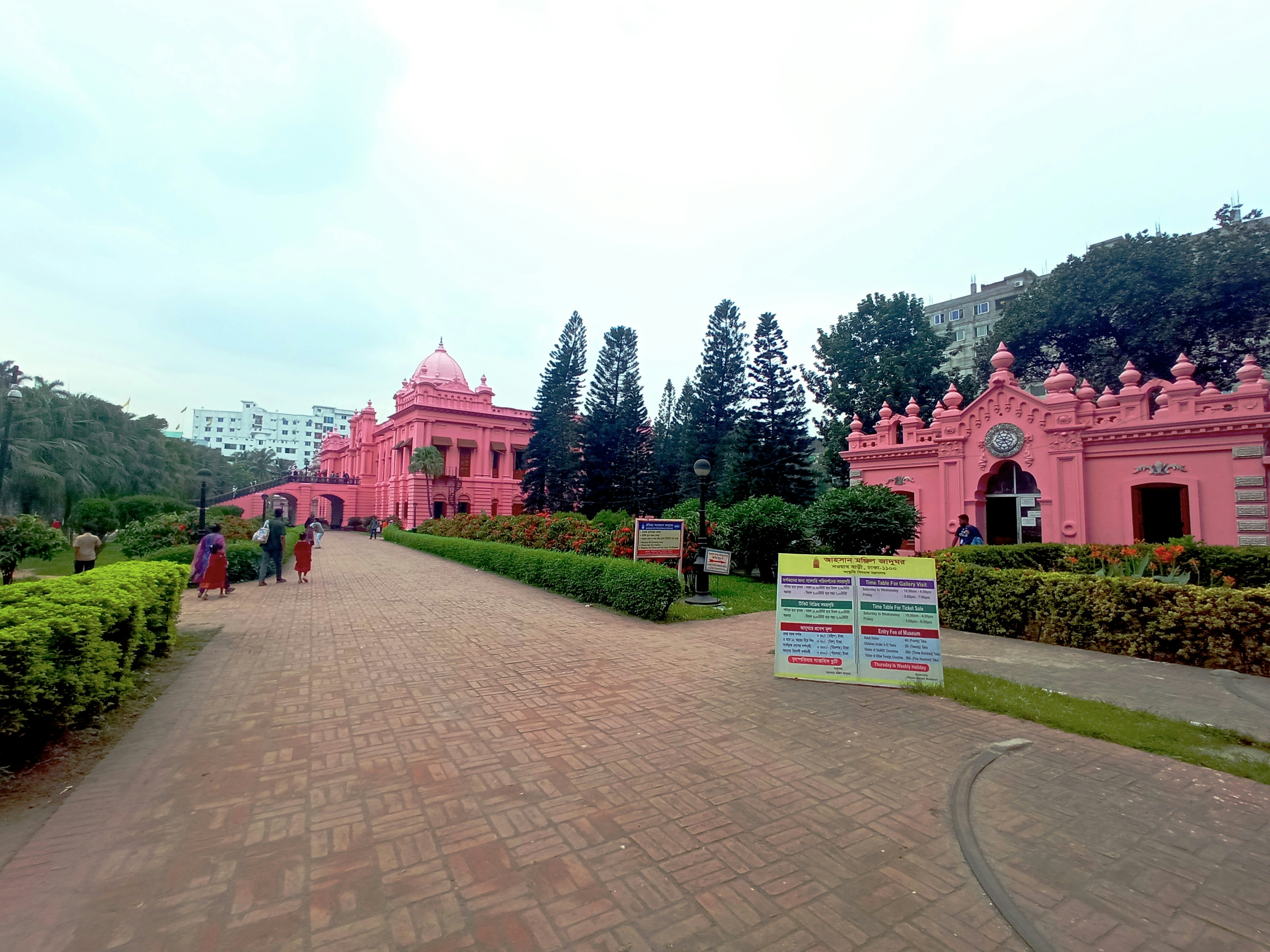 Historical pink palace with ornate architecture surrounded by gardens and trees on a cloudy day.