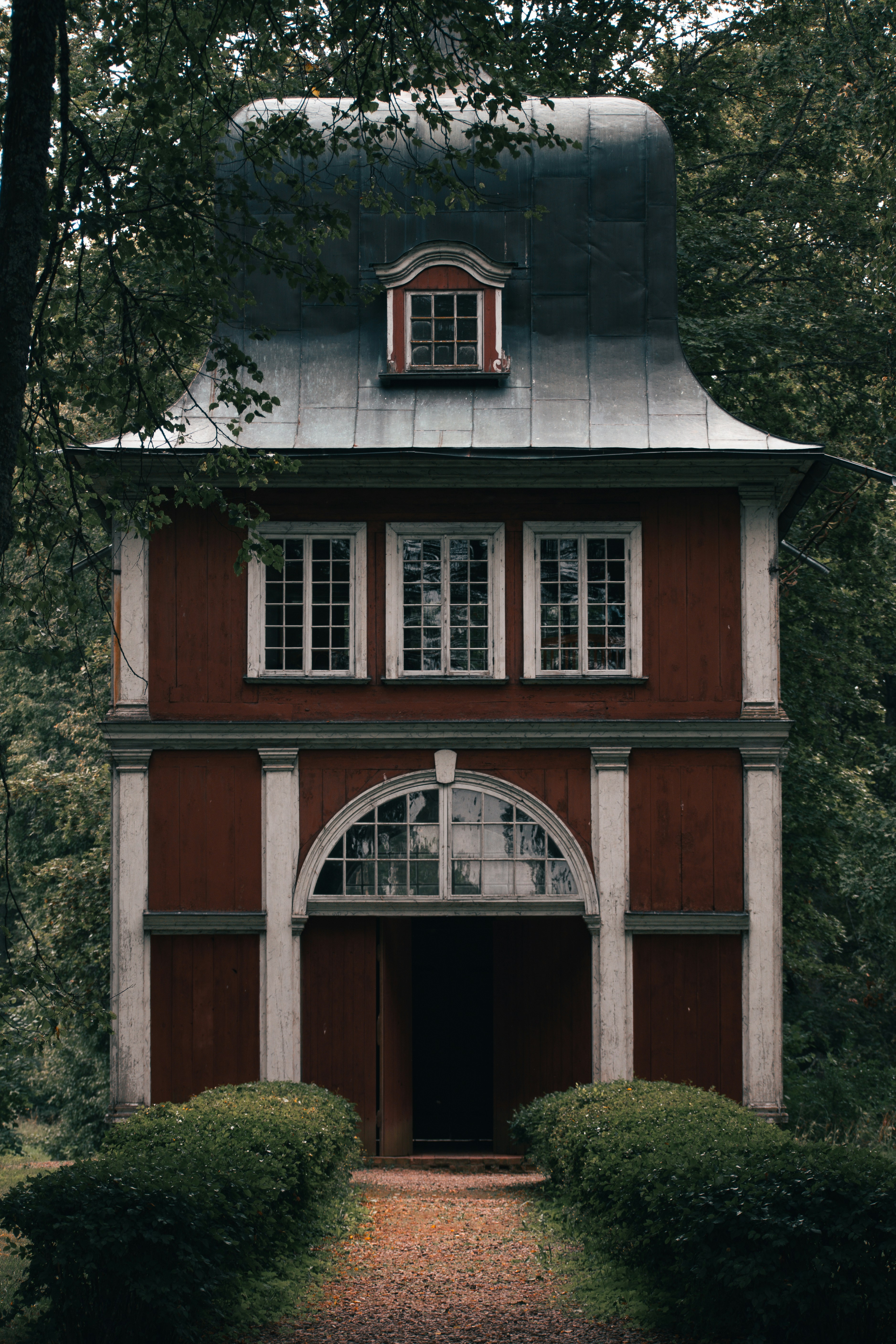 An elegant wooden structure with a distinctive curved roof, framed by lush greenery, invites exploration. The entrance hints at stories waiting to be uncovered.