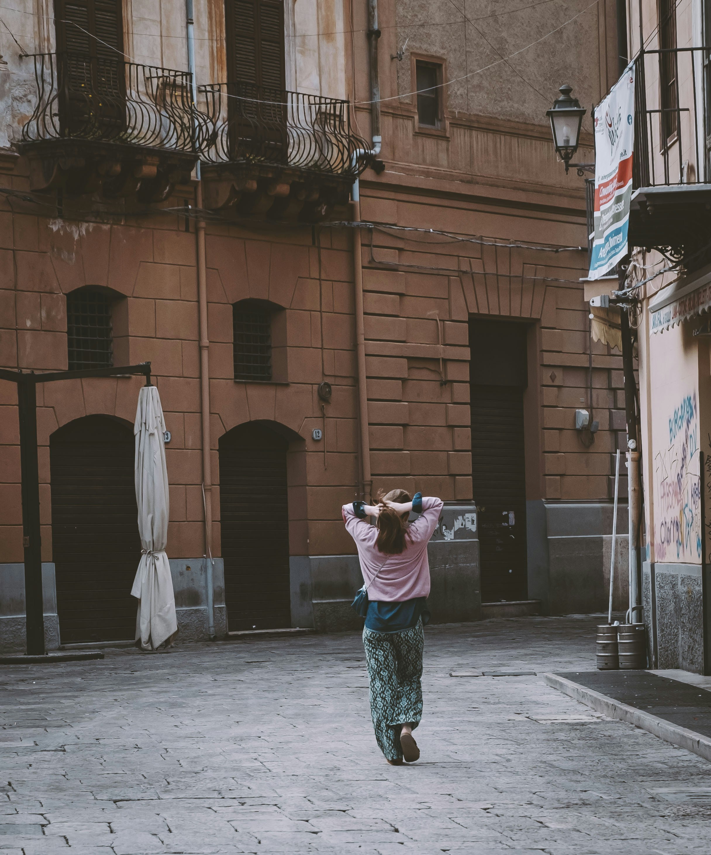 Person in colorful attire walking down a narrow, cobblestone alley lined with aged buildings.