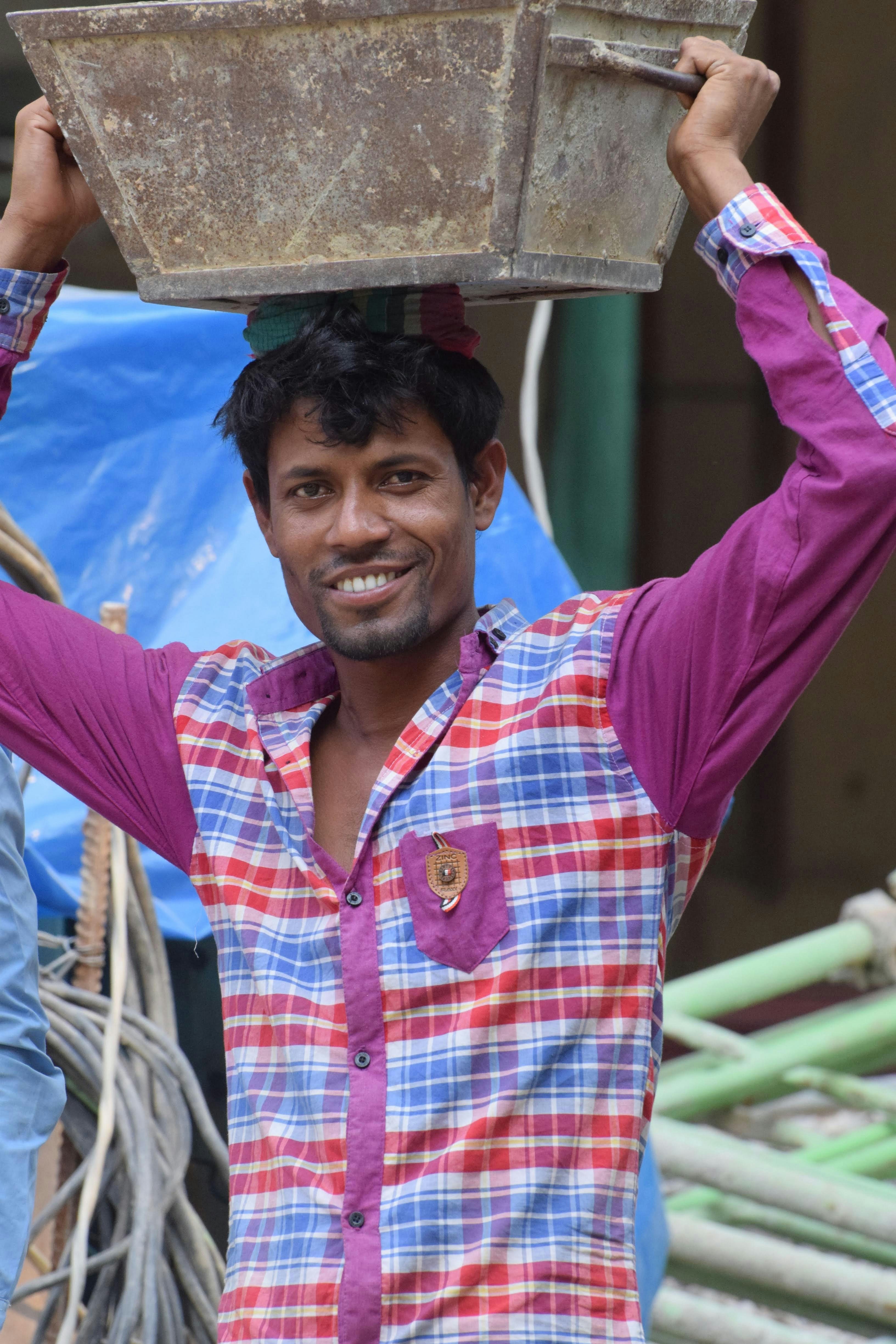 Joy in the Lift: A Colorful Worker Hoists a Dusty Bucket in a Makeshift Workshop