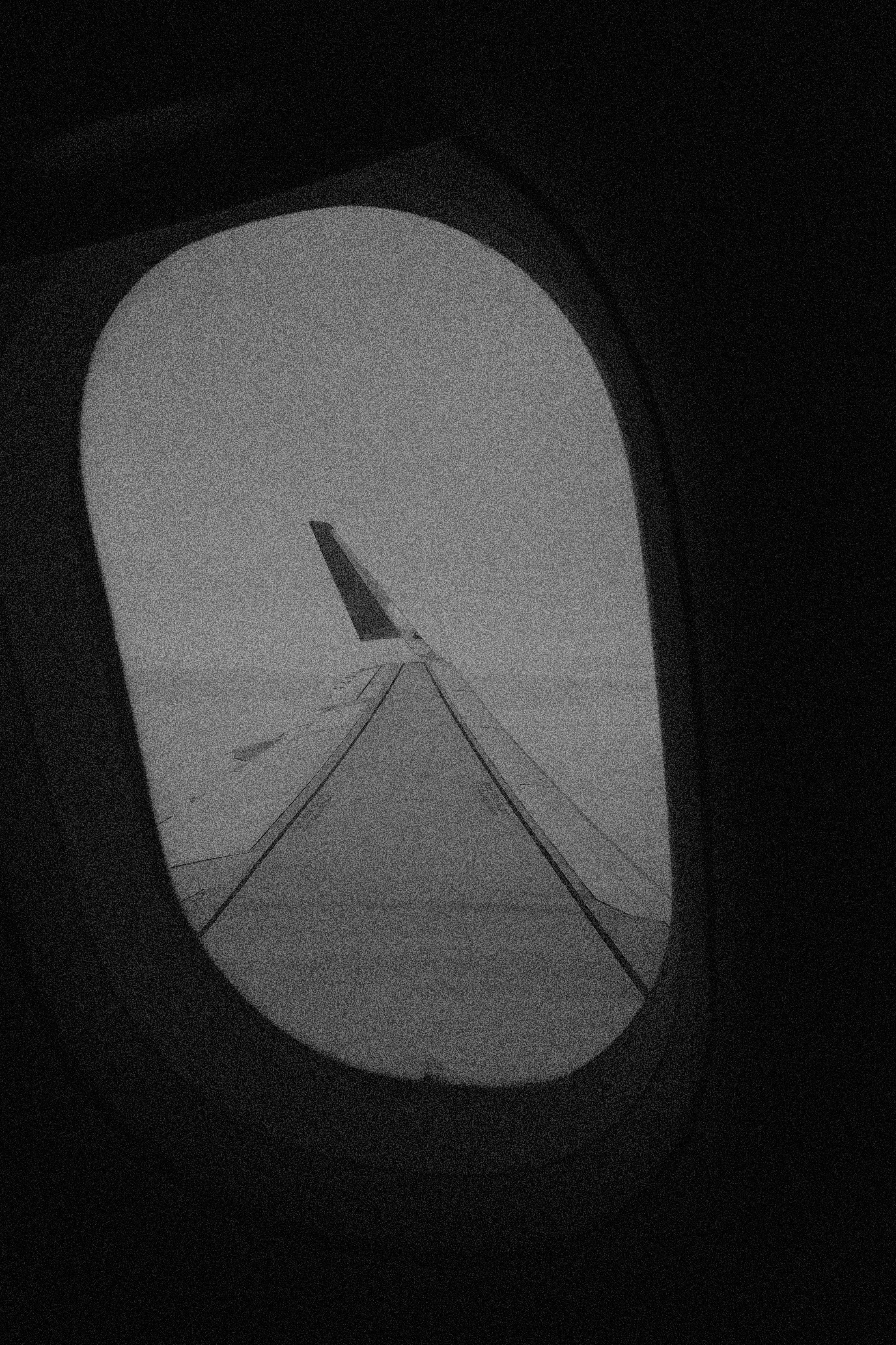 View from an airplane window showcasing the wing and a blanket of clouds in monochrome tones.