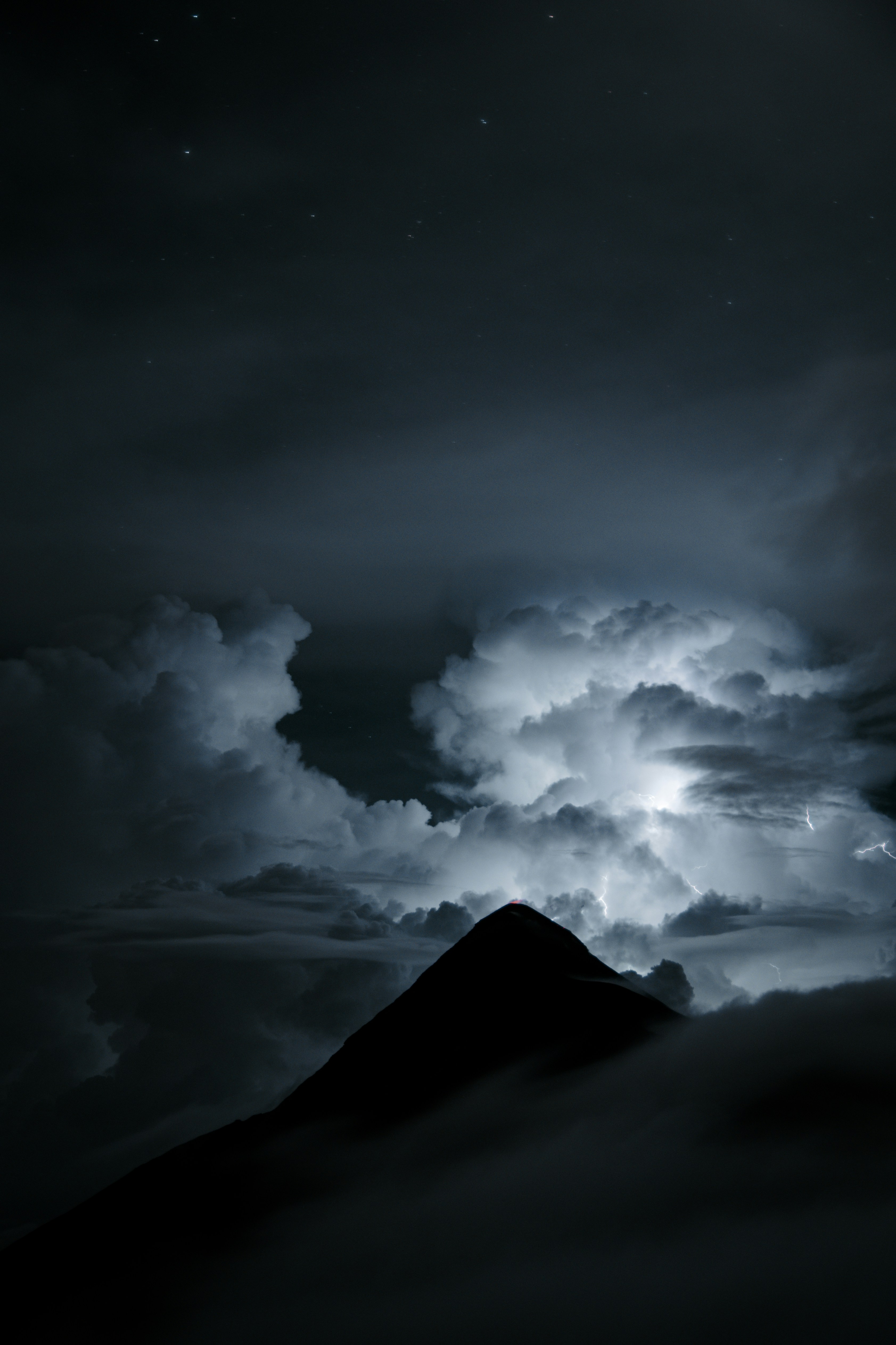 A dramatic mountain silhouette rises against a backdrop of illuminated storm clouds, capturing the essence of nature's power and mystery.