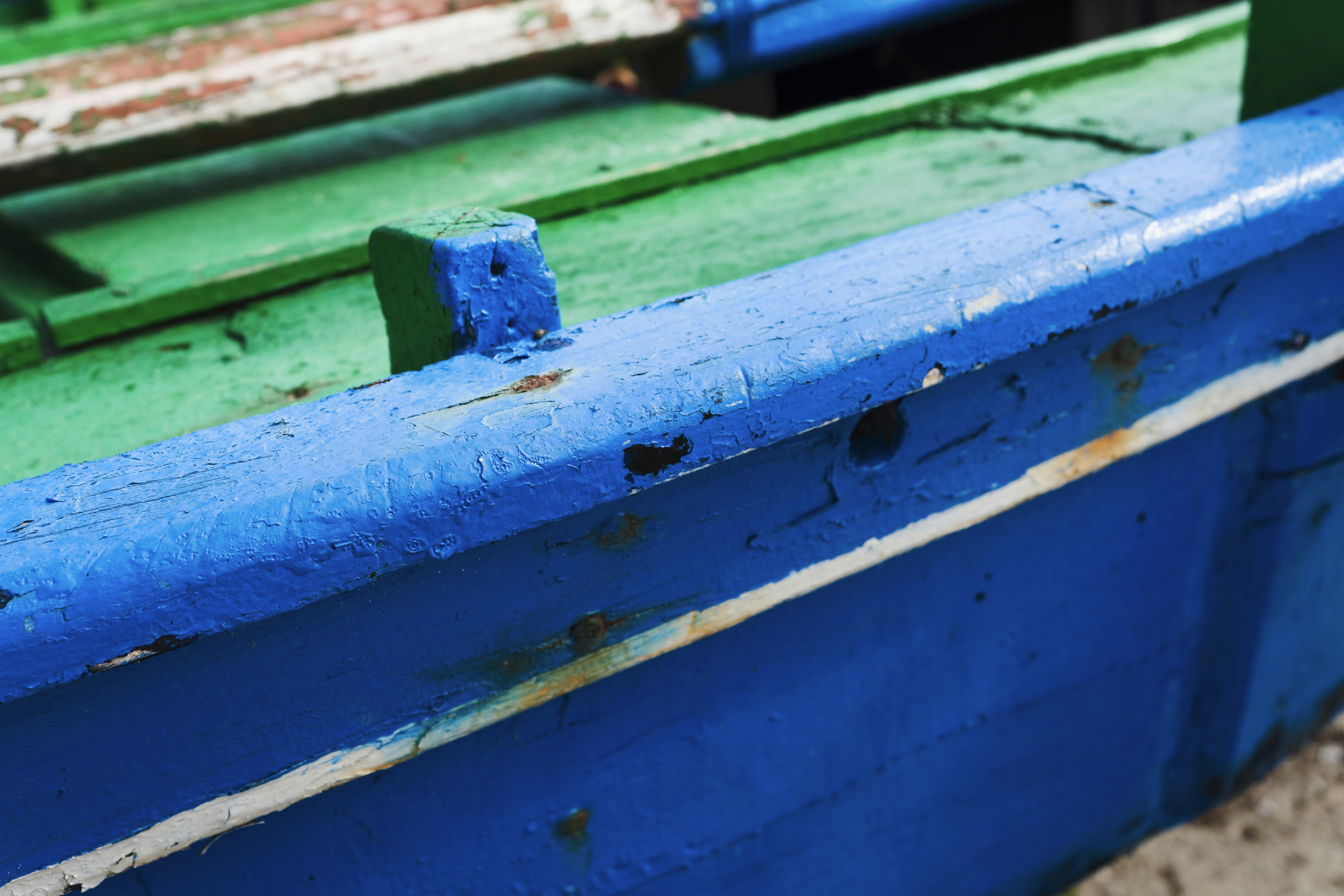 Blue And Green Wooden Boat Close Up - The image shows a close up of a wooden boat that has been painted blue and green. The boat is weathered and shows signs of age and use. The paint is chipping and peeling in places, revealing the wood underneath.