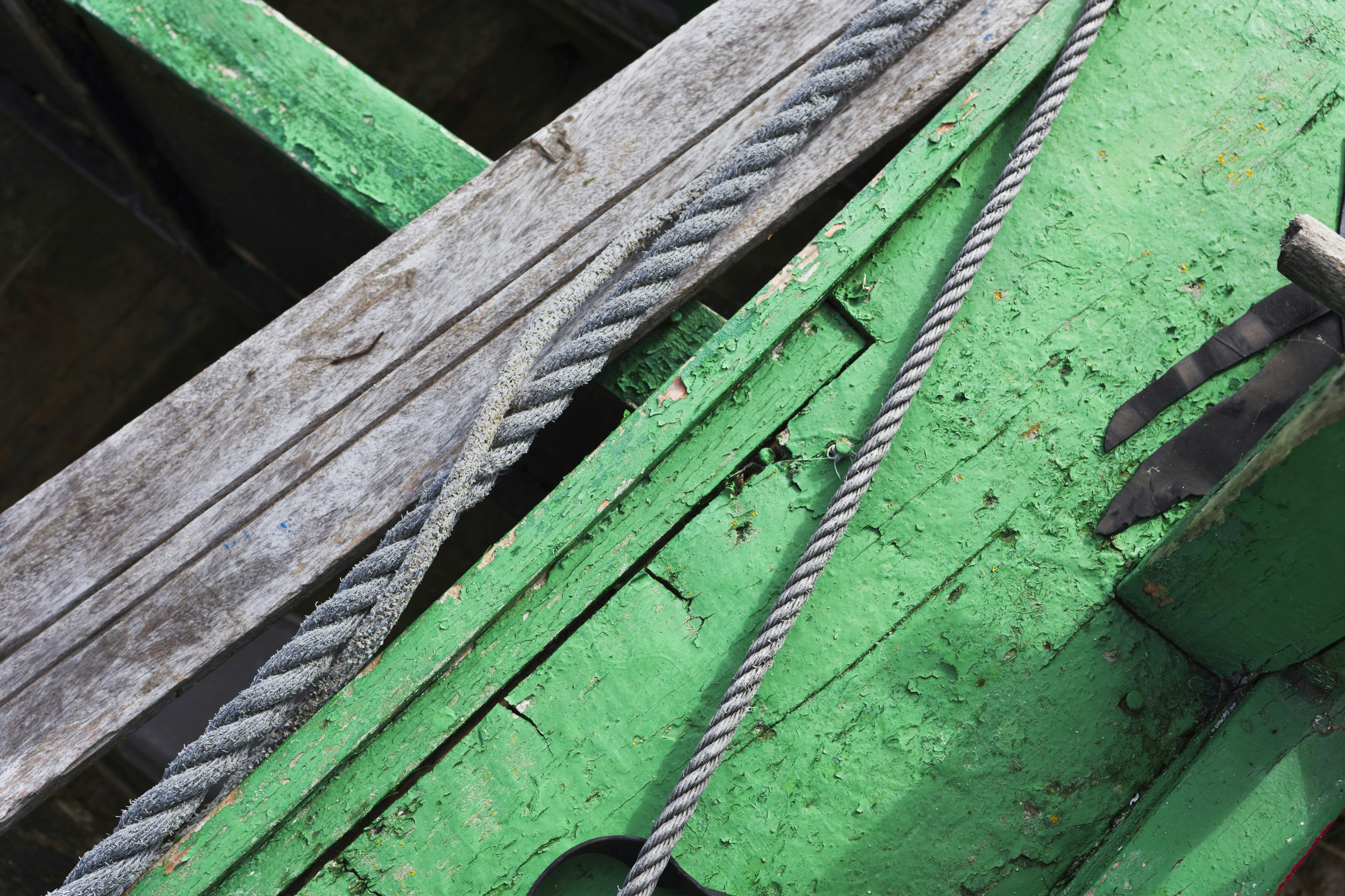 Weathered green wooden boat with cracked paint and diagonally placed ropes revealing wood beneath.