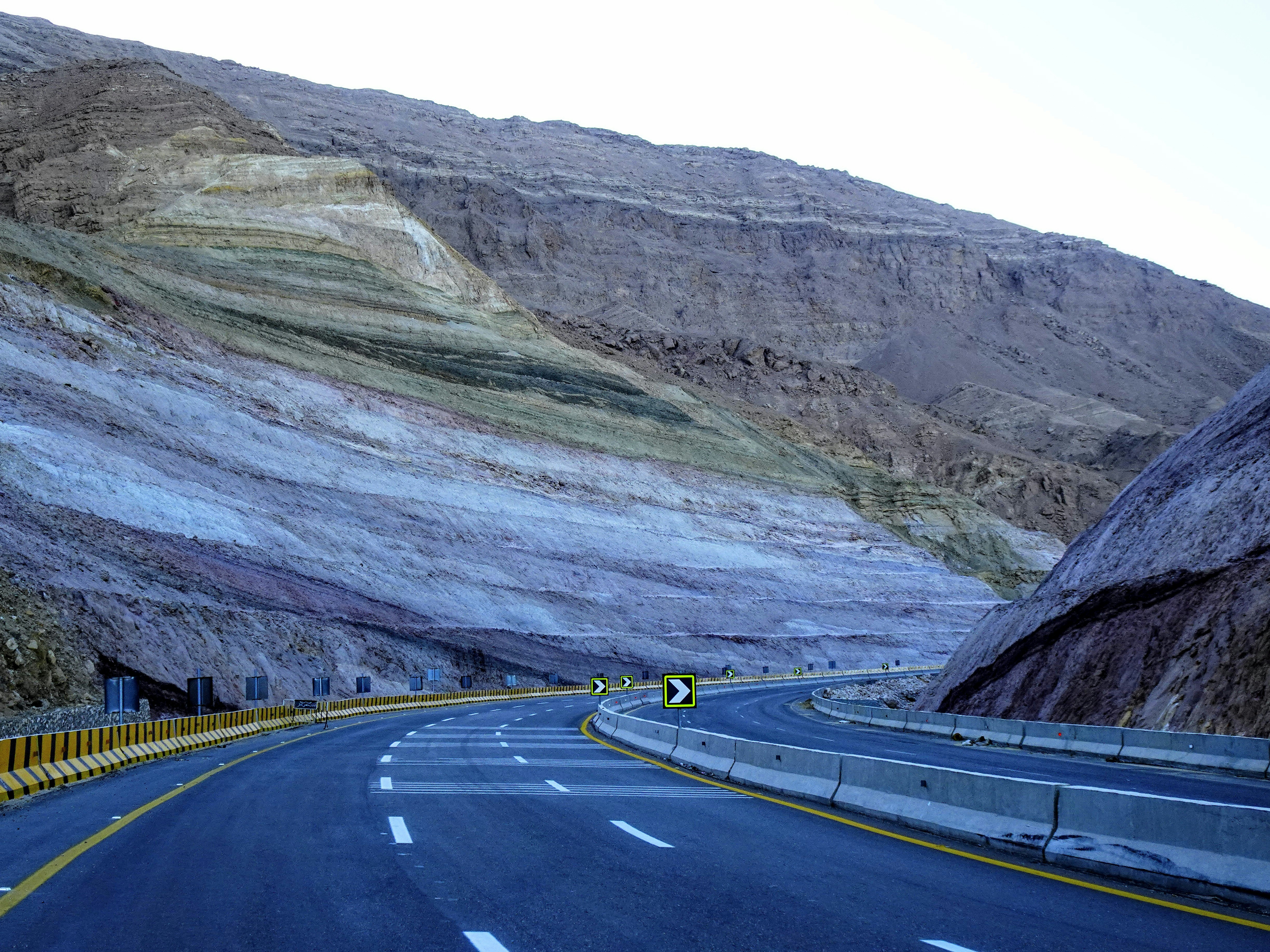 Curving road nestled between colorful layered rock formations, showcasing the geological history of the region.