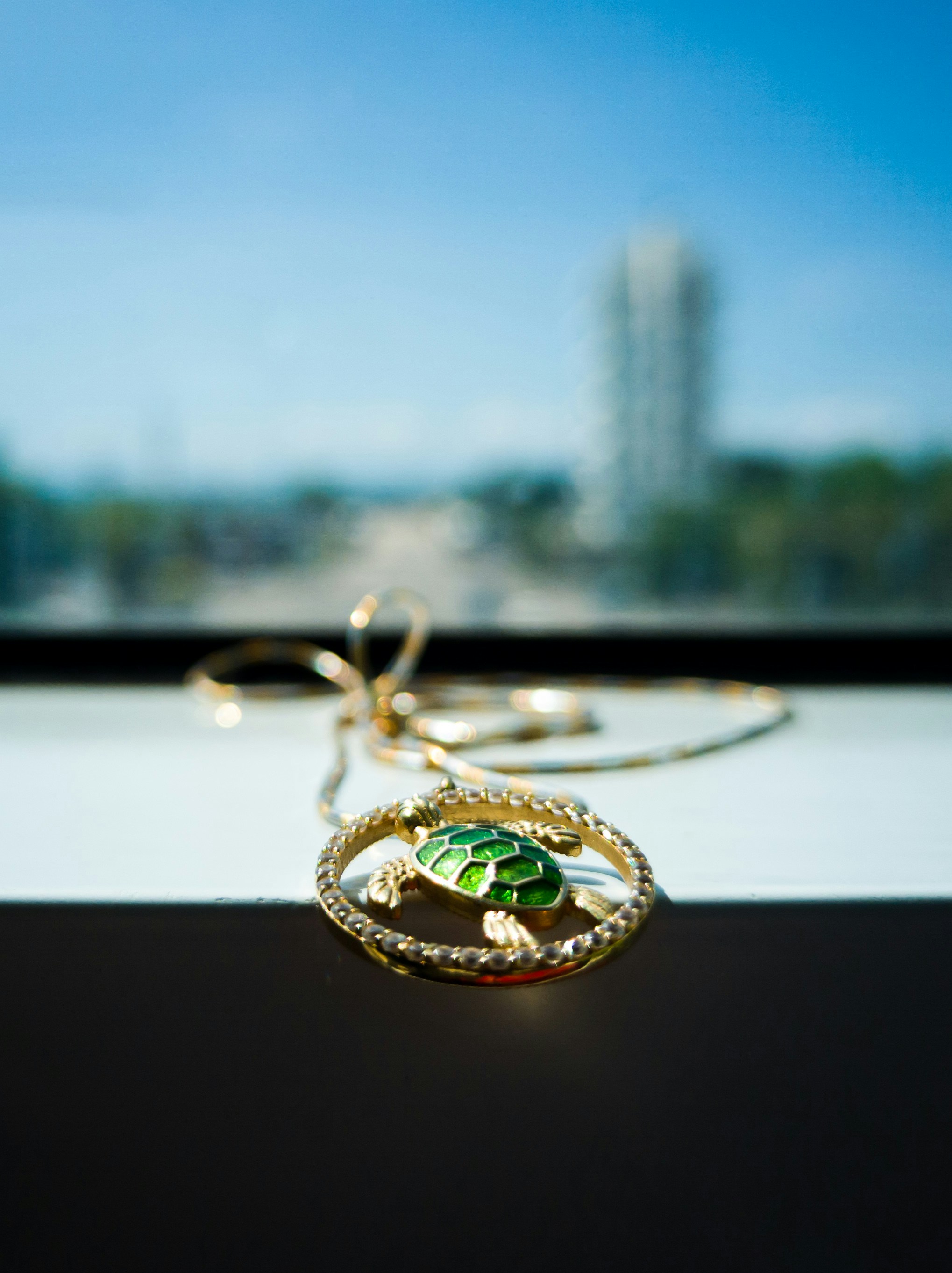 Emerald Pendant on a Golden Coil, framed by a softly blurred city skyline