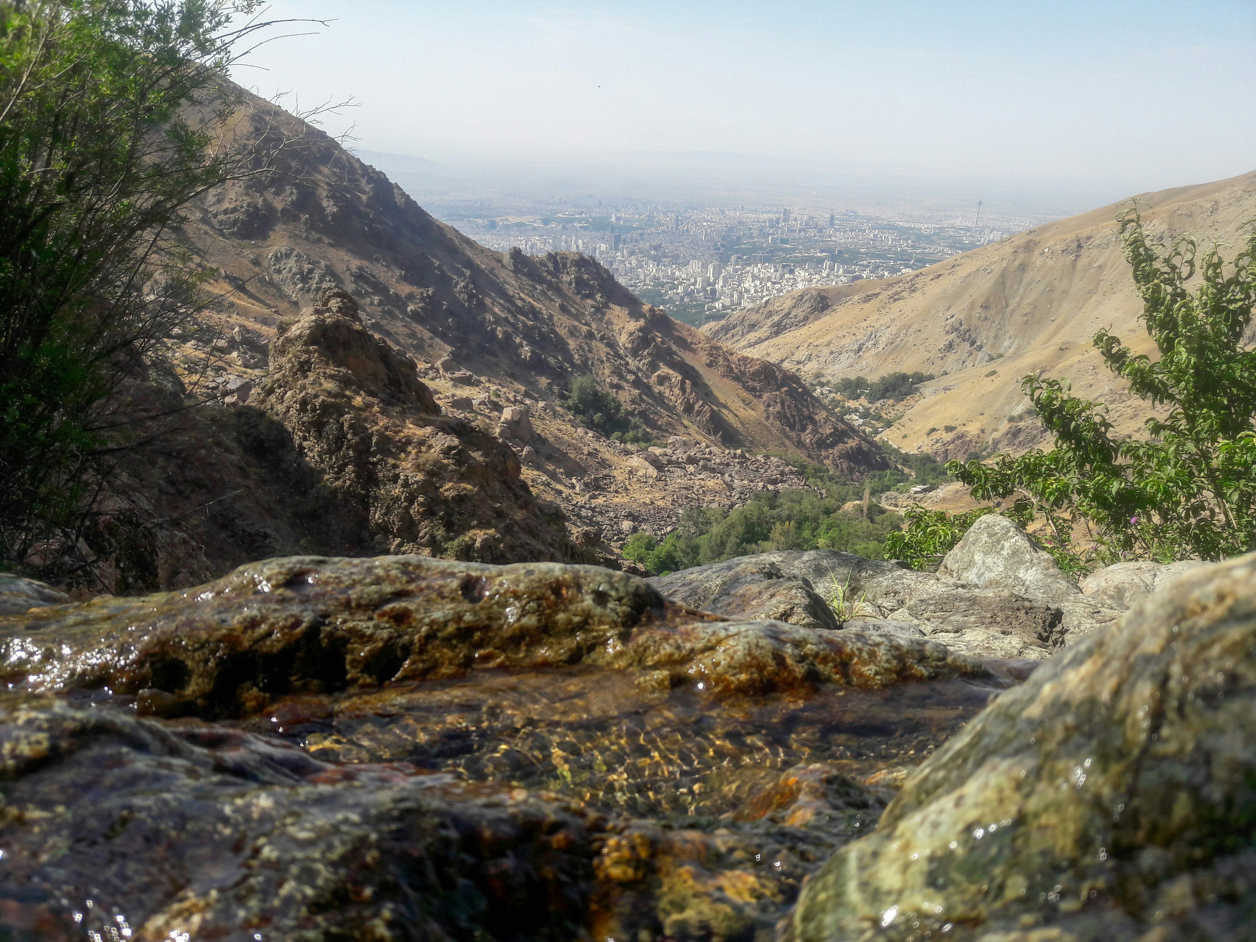 Flowing water in the foreground with a panoramic view of a sprawling city nestled between rugged mountains. The scene captures the harmony between nature and urban life.