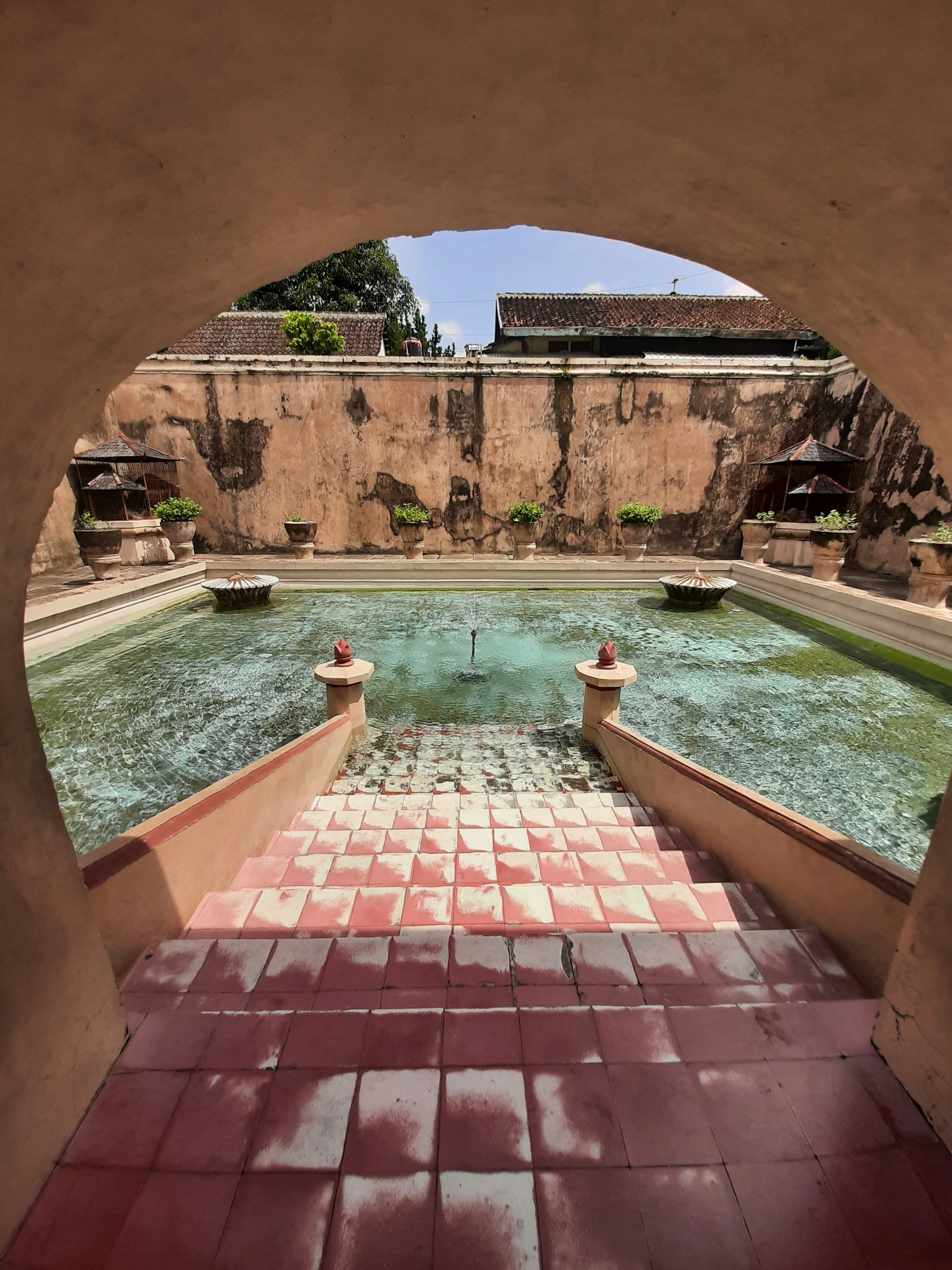 Archway Descent: Pink Tiles Framing a Weathered Courtyard Fountain
