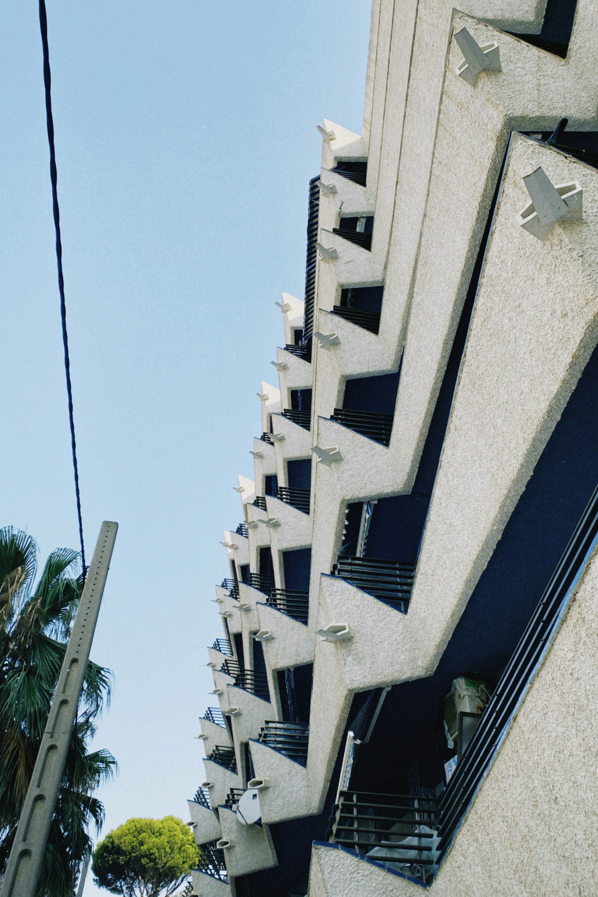 Abstract view of a uniquely designed building showcasing angular balconies against a clear blue sky.
