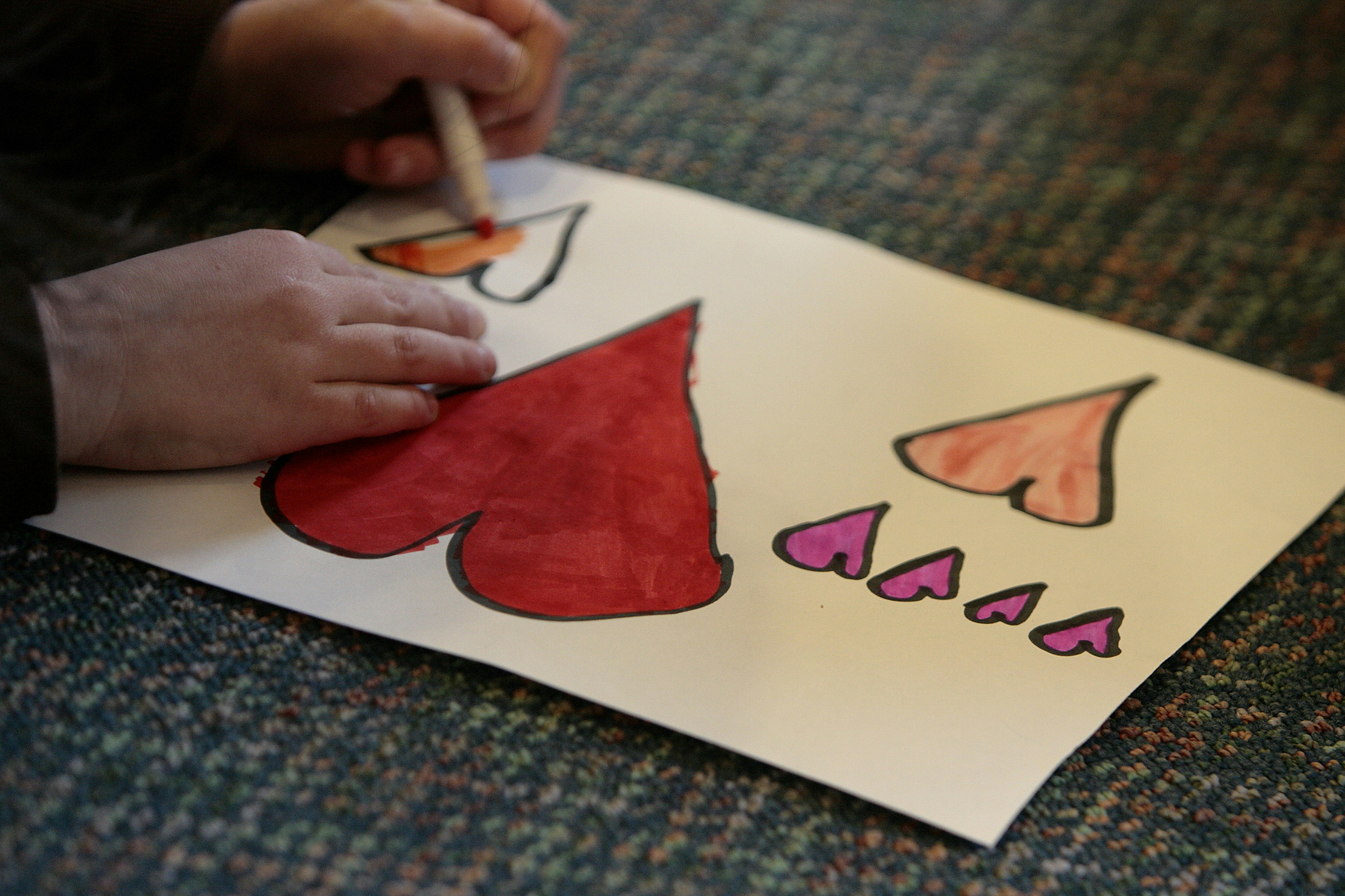 Child coloring red and pink hearts on white paper with a marker.