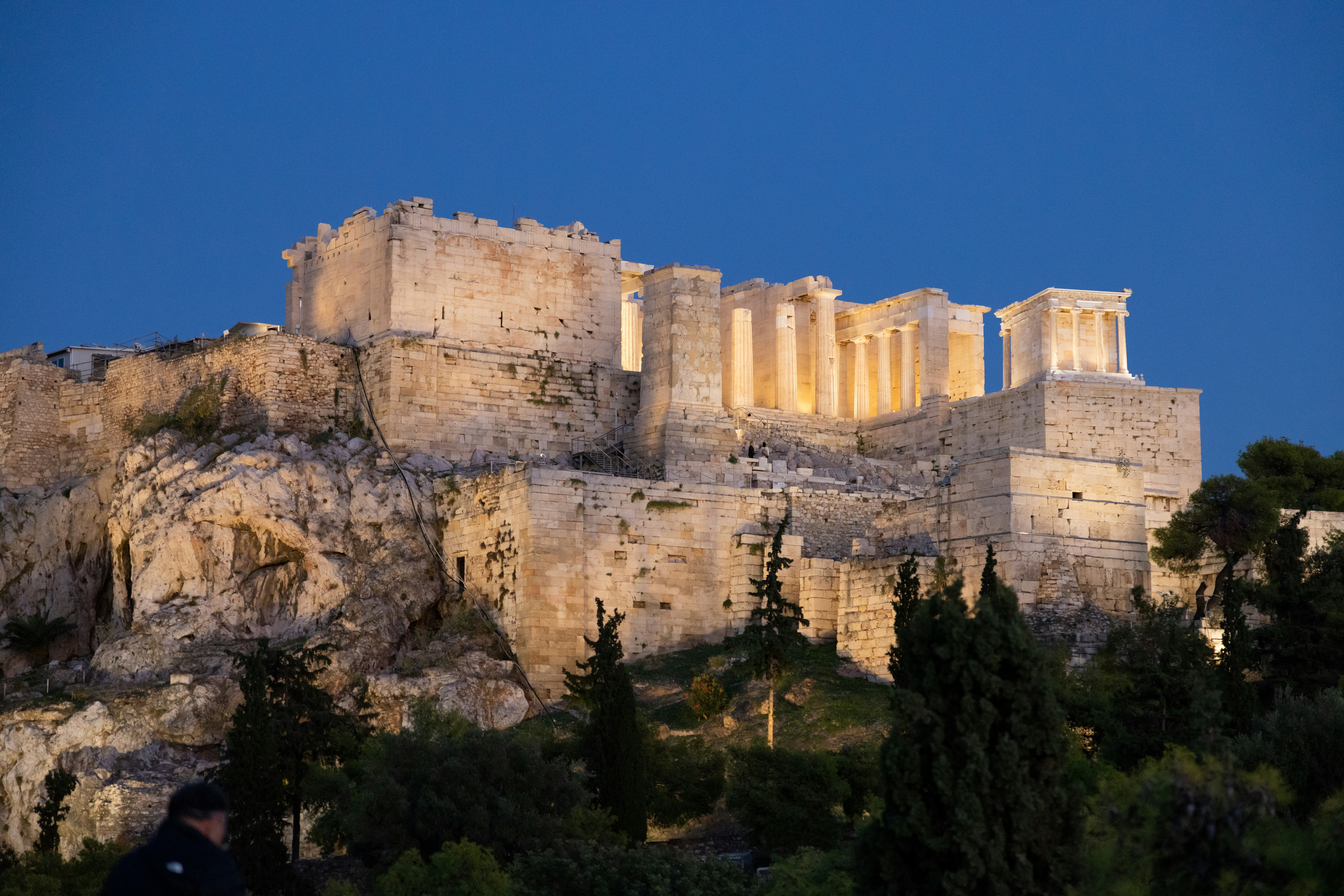 A stone building on a cliff with Acropolis of Athens in the background ...