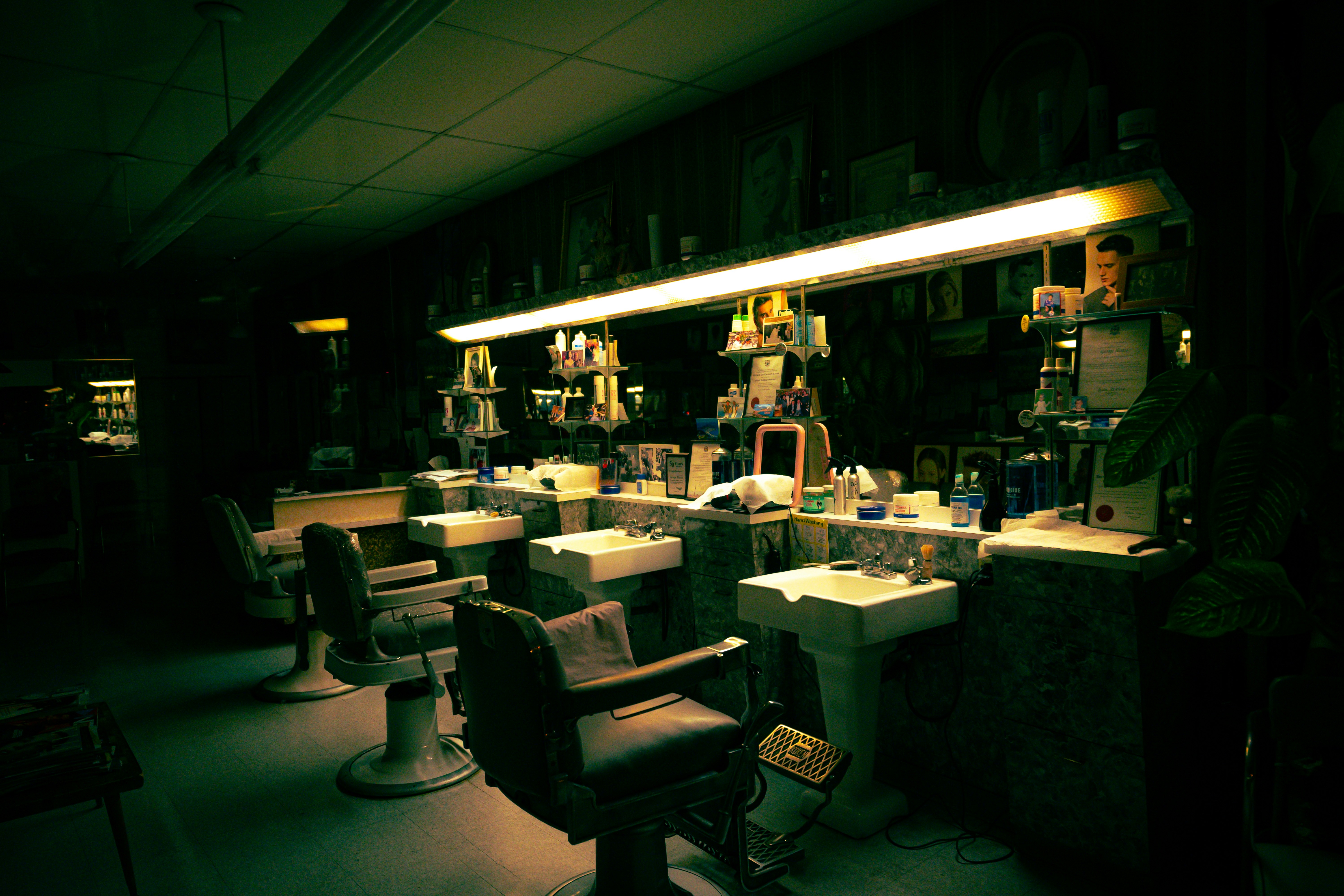 Dimly lit barber shop featuring vintage styling chairs and a long illuminated mirror, surrounded by nostalgic decor.