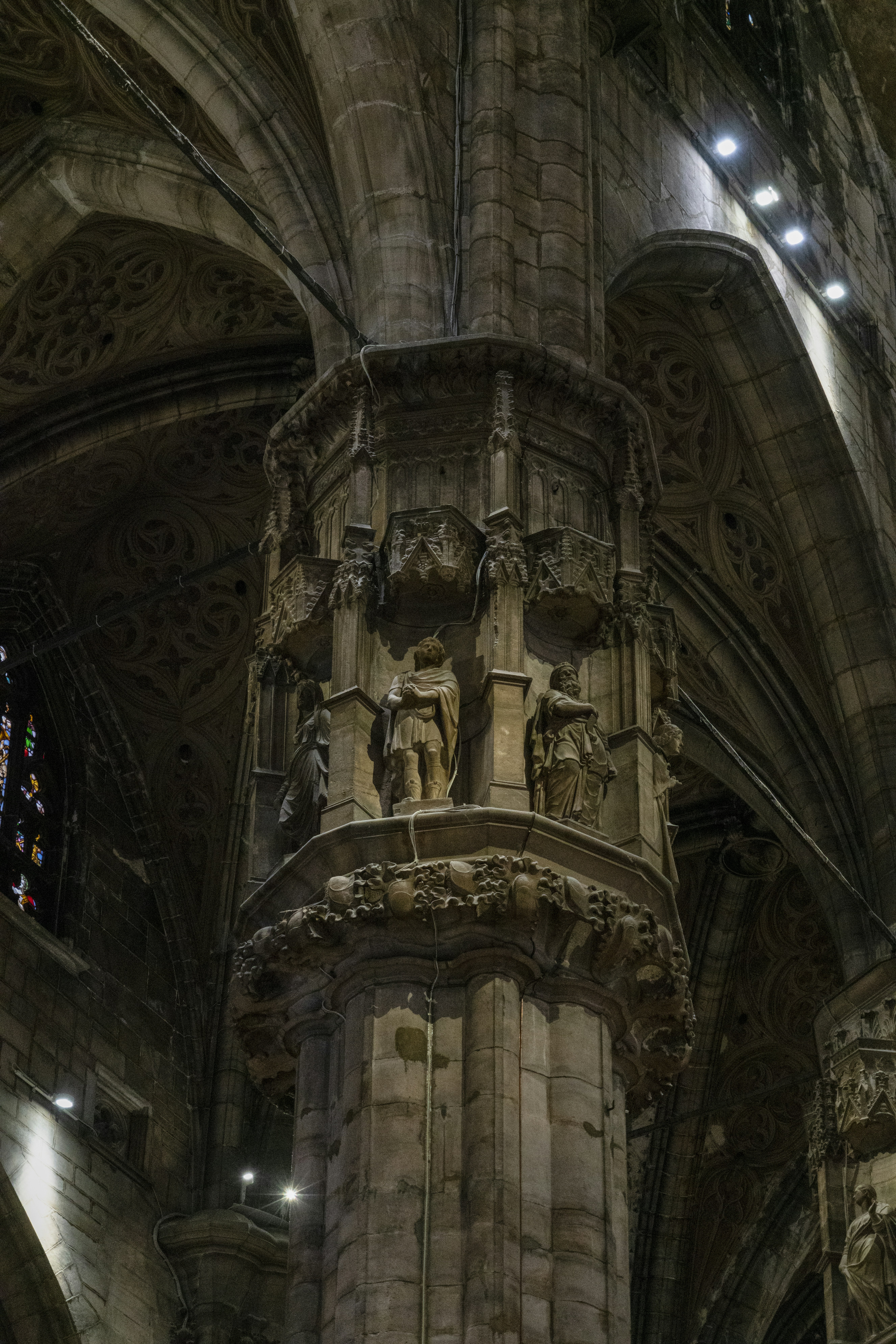 Guardians of Stone: Sculpted Figures Crown a Gothic Pillar Beneath Cathedral Arches
